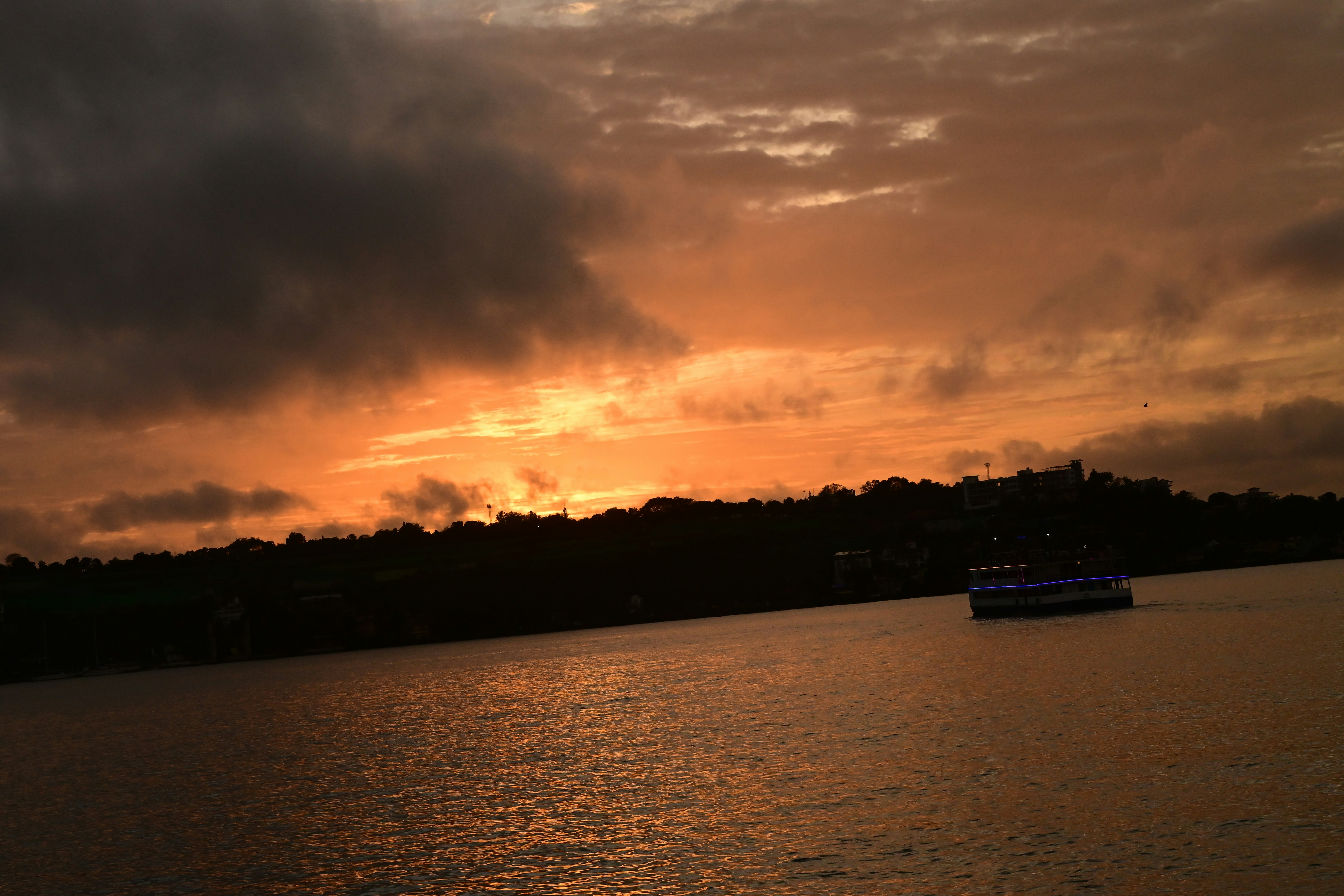 A serene sunset over a calm lake, with a boat gently gliding across the shimmering surface. The sky is painted in warm hues of orange and gold, contrasting with the darkening landscape.