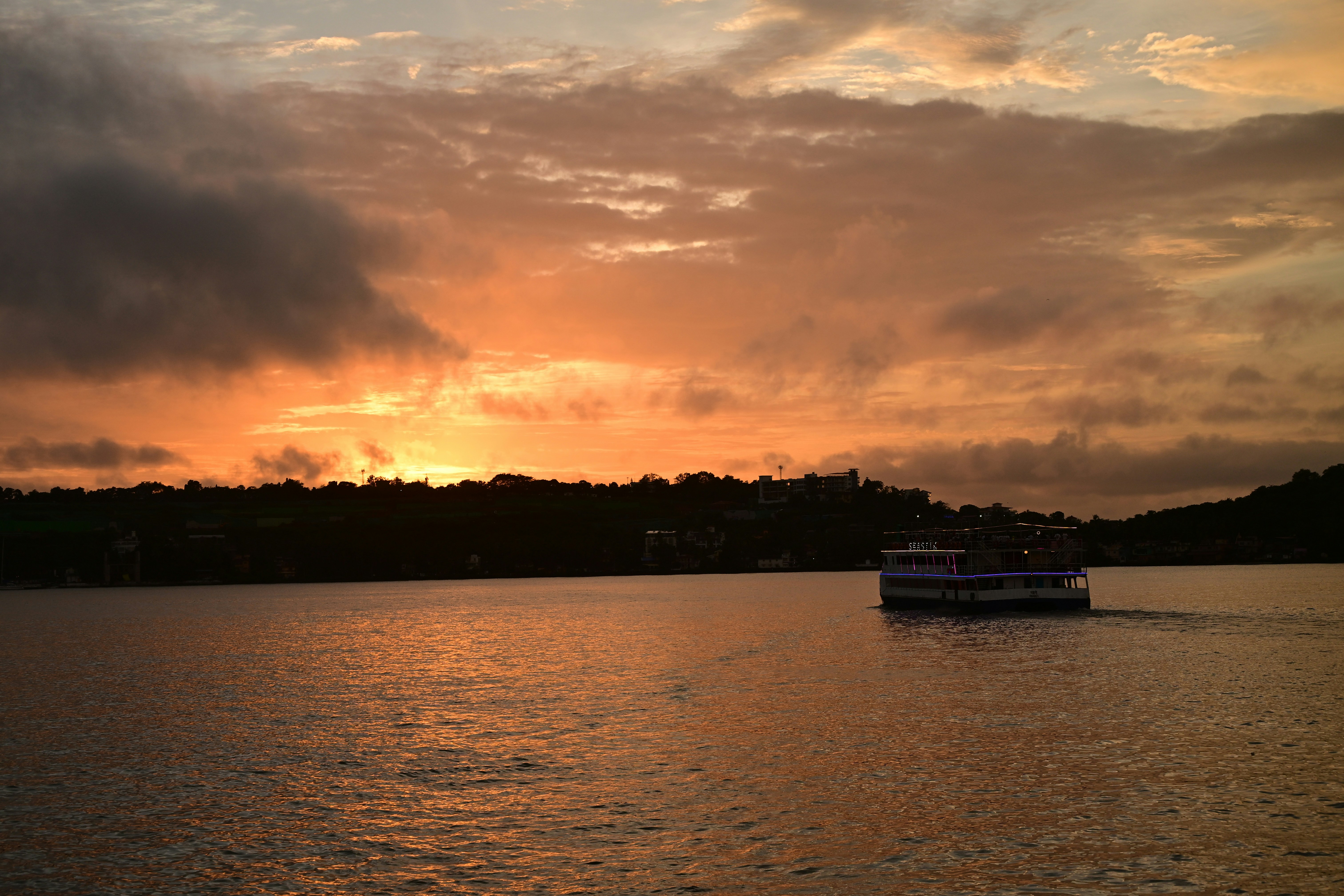 A boat gliding across a shimmering lake under a vibrant sunset, with clouds casting shadows on the horizon.