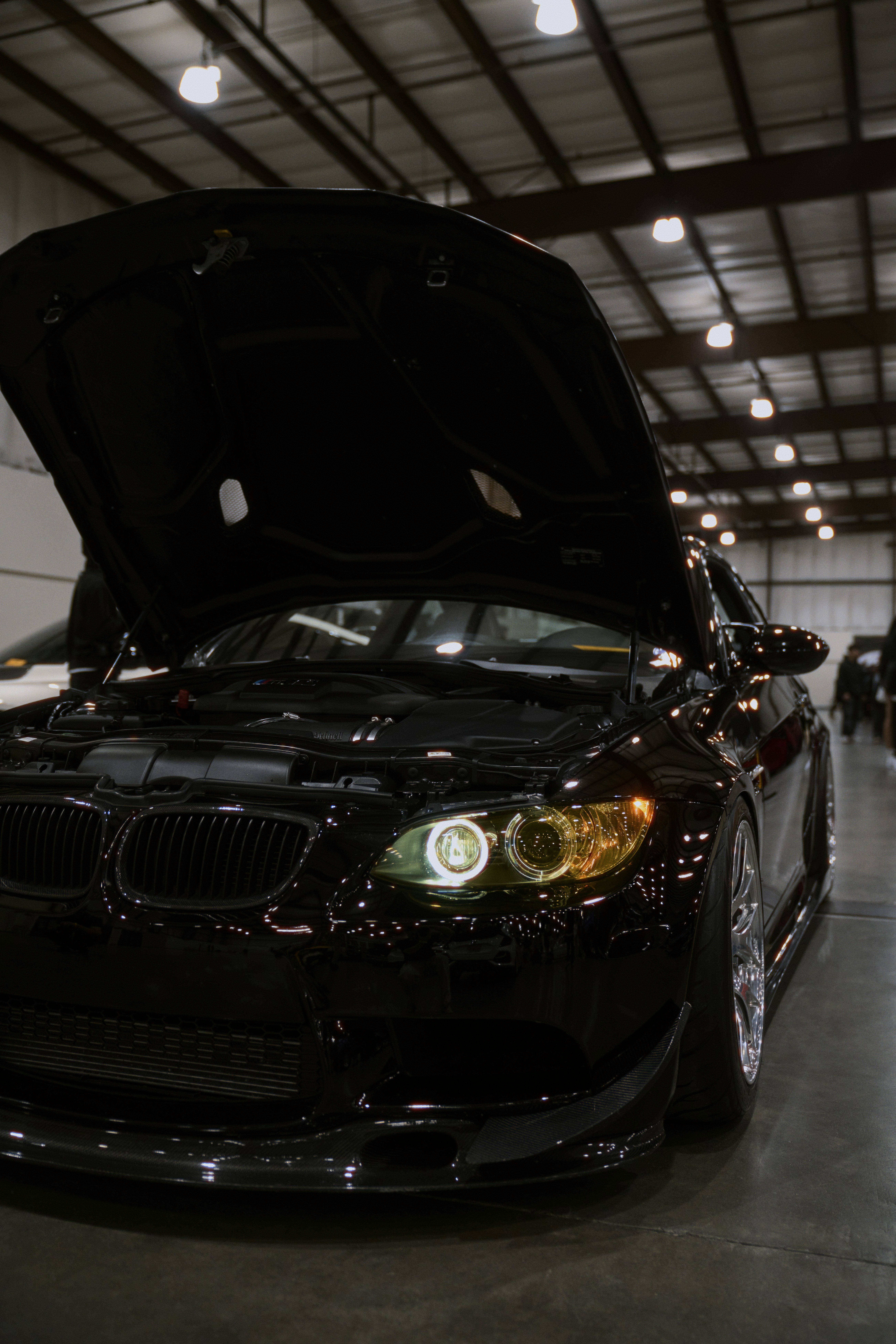 Modified black car with hood raised, showcasing the engine compartment in a well-lit indoor setting.
