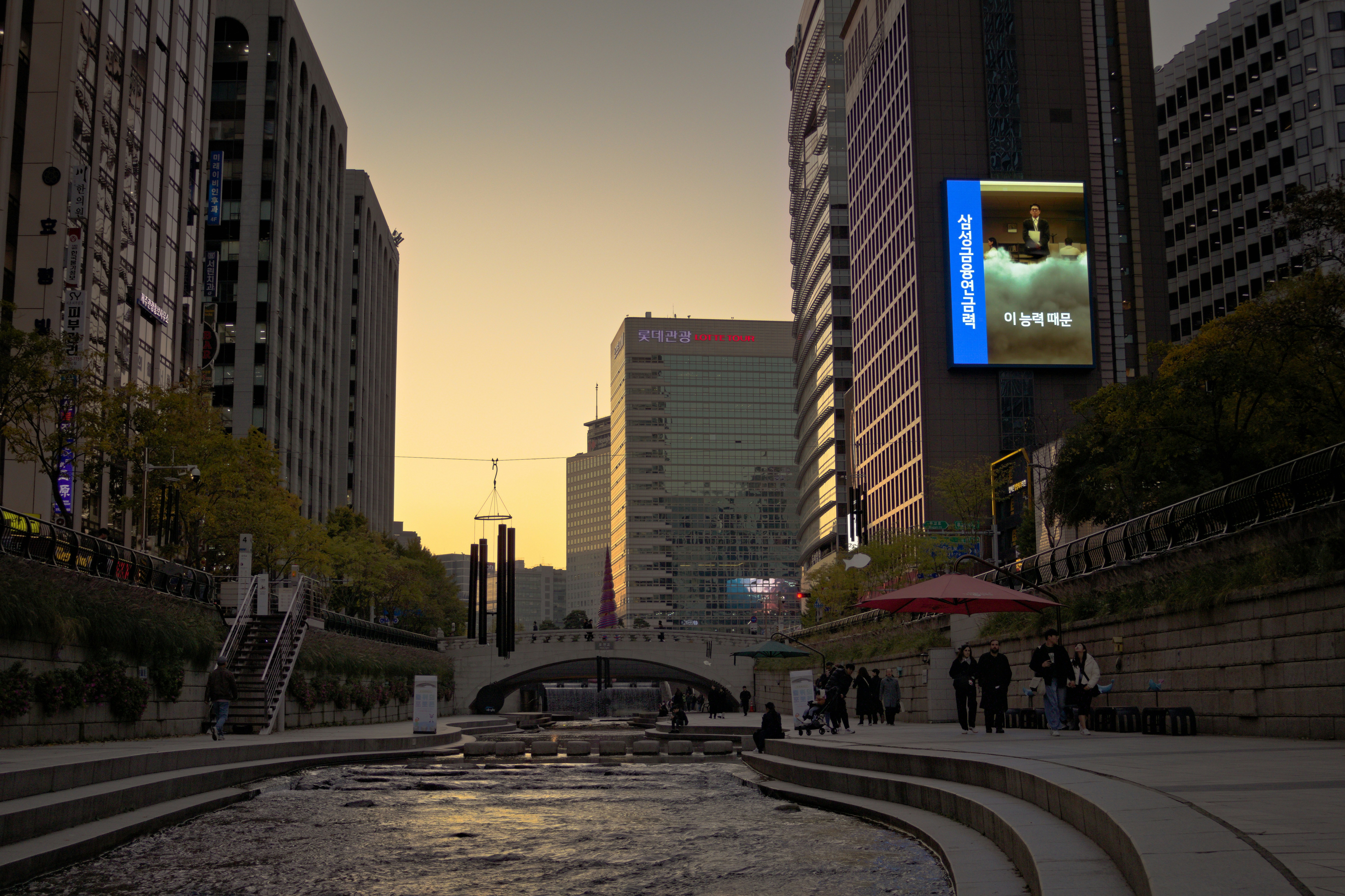 Cityscape showcasing a tranquil waterway bordered by modern buildings, illuminated by the soft glow of sunset. A digital billboard adds a contemporary touch.