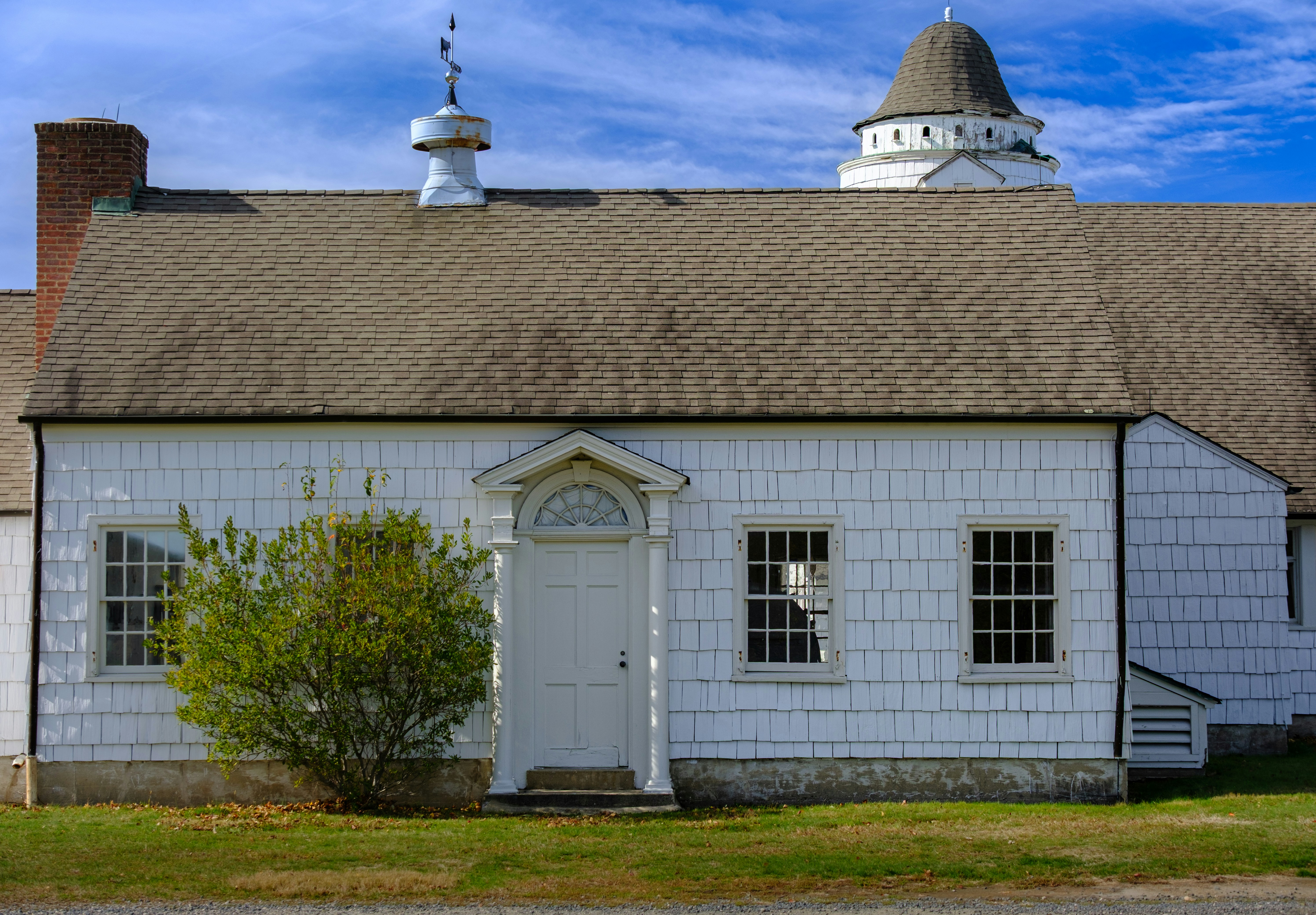Classic white clapboard house with a distinctive cupola and surrounding greenery, embodying rustic charm and historical significance.