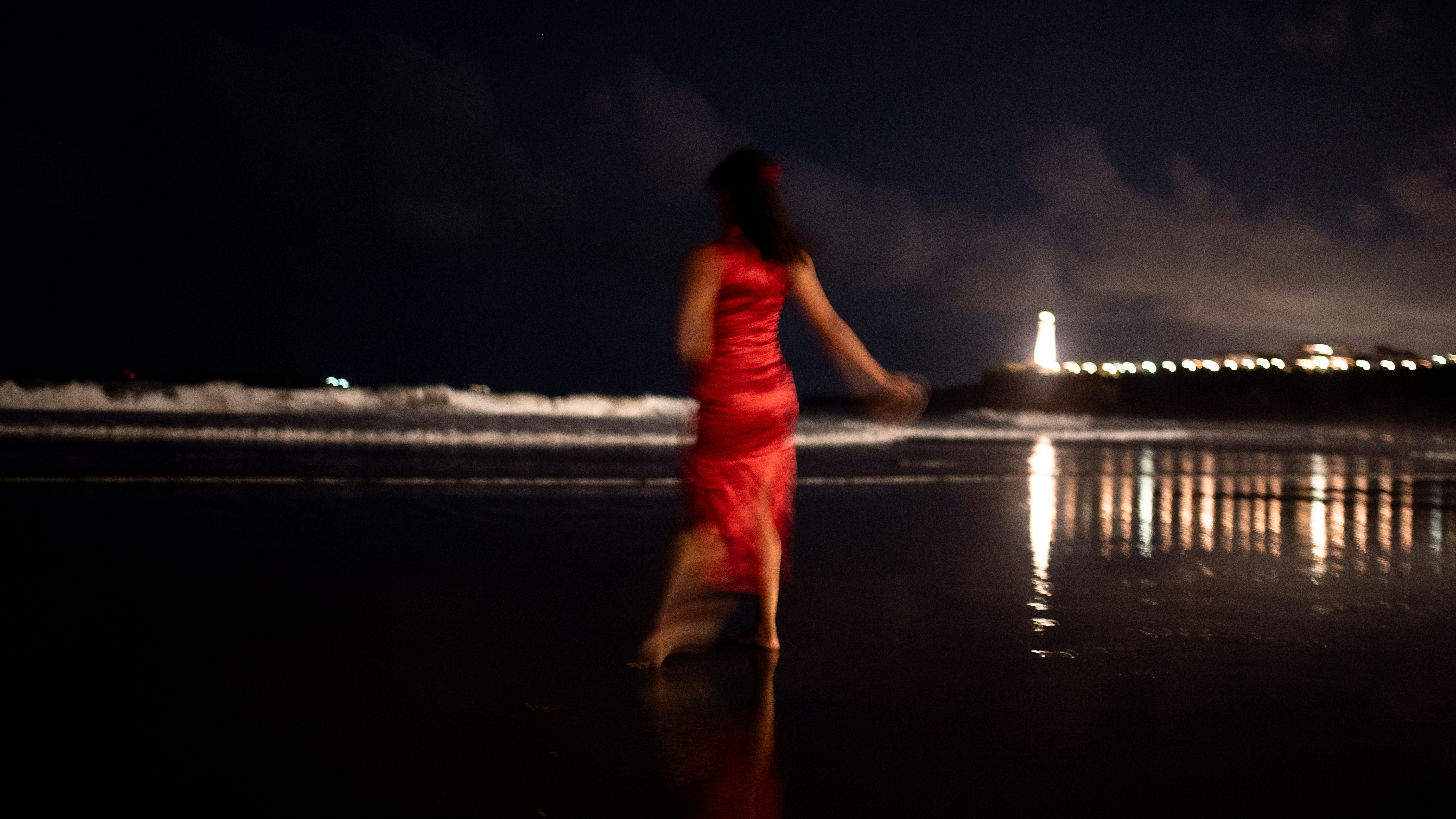 Woman in red dress dances on beach at night.