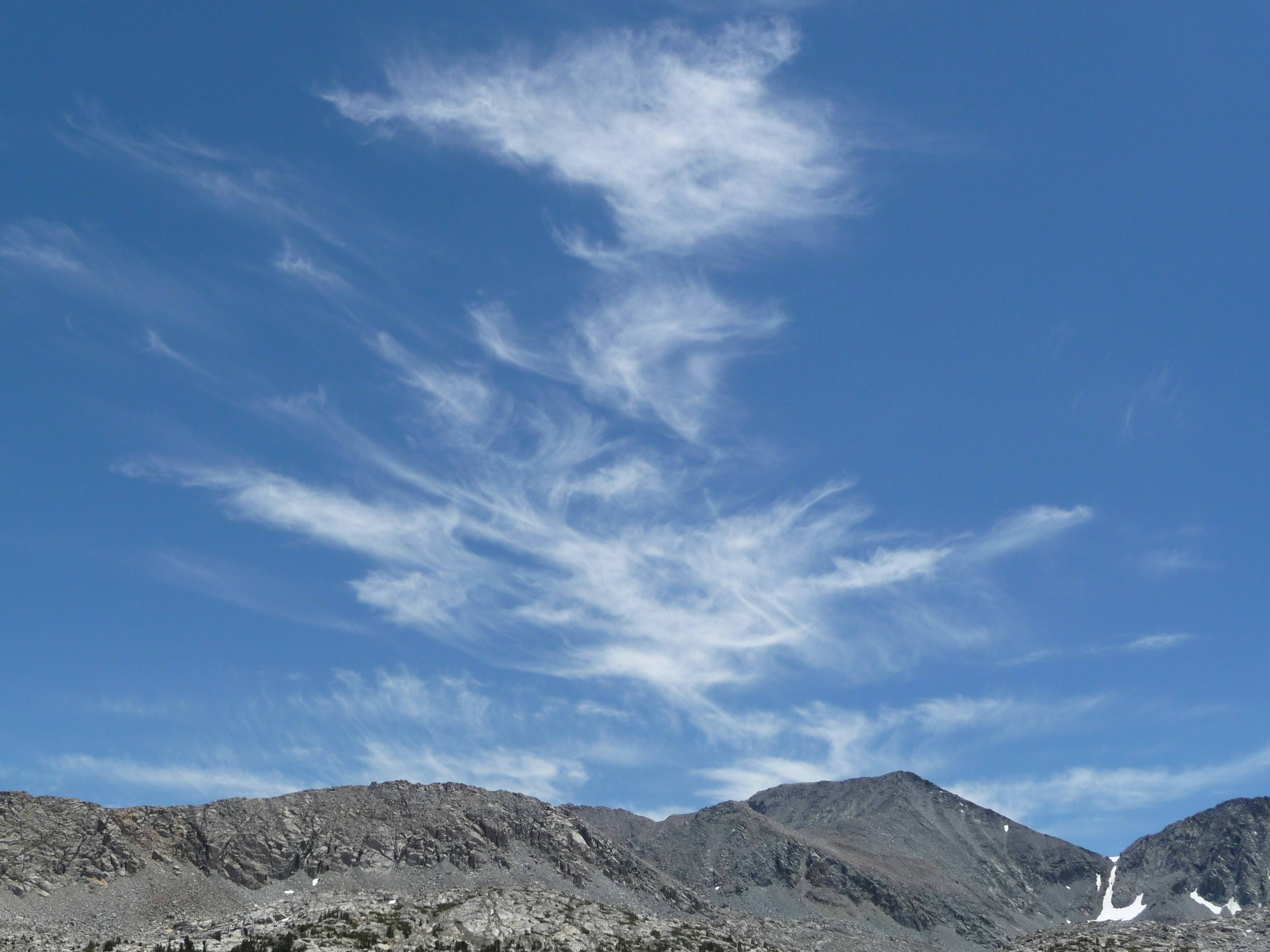 Wispy clouds drift across a clear blue sky above mountains.