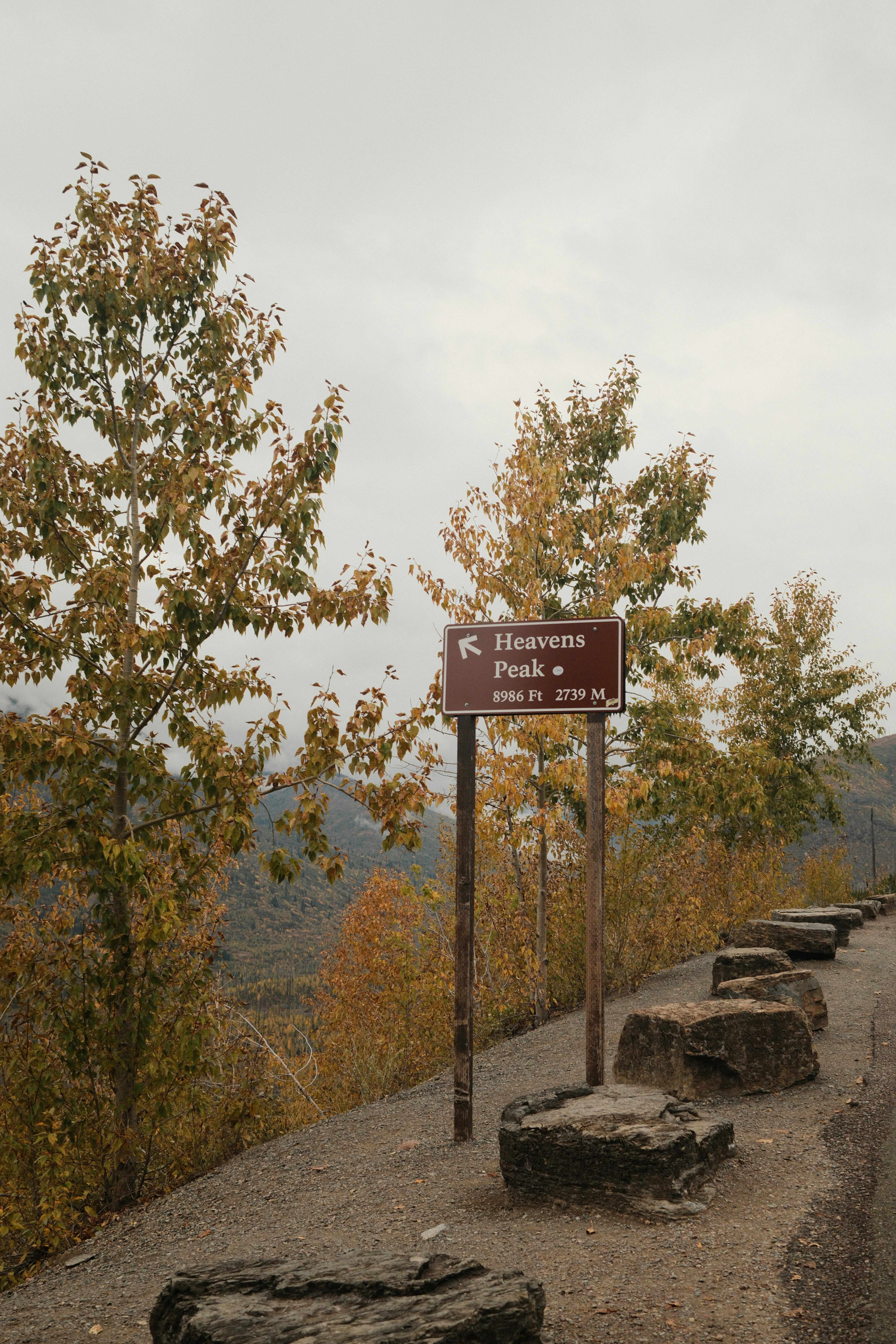 Signpost indicating the direction to Heavens Peak, surrounded by autumn foliage and rocky benches along a scenic overlook.