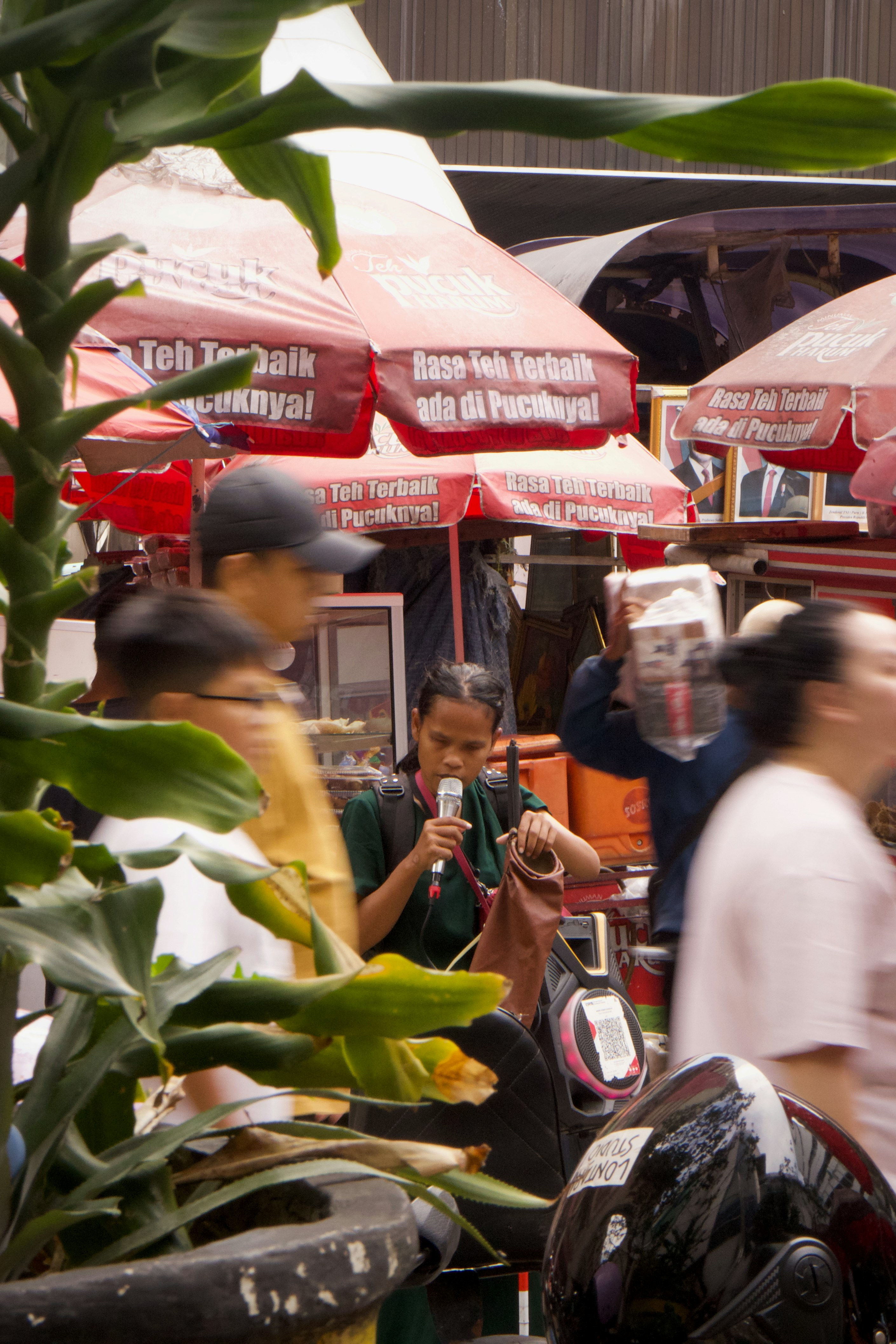 People walking past outdoor food stalls with red umbrellas.