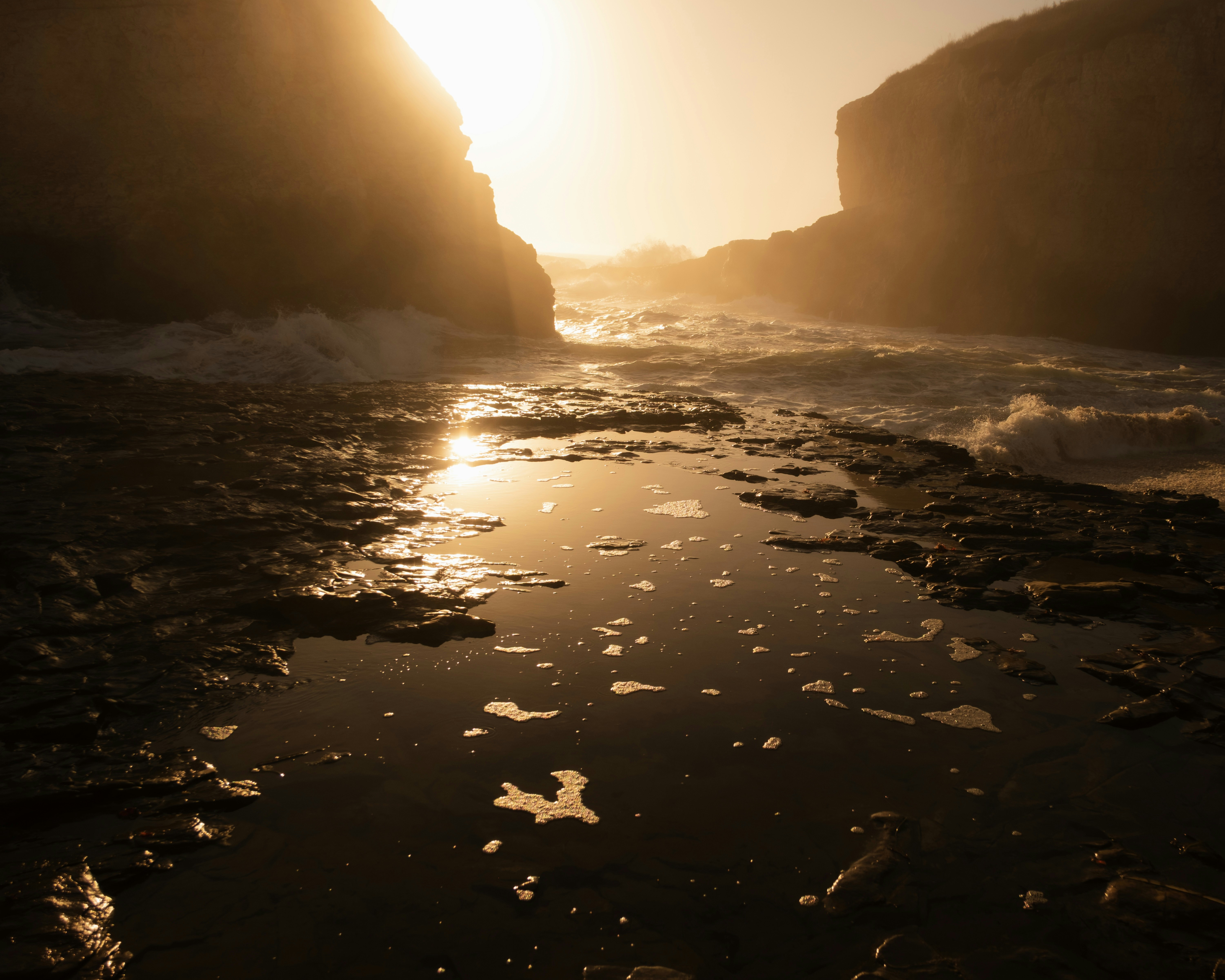 Golden sunset illuminates waves crashing against rocky shore