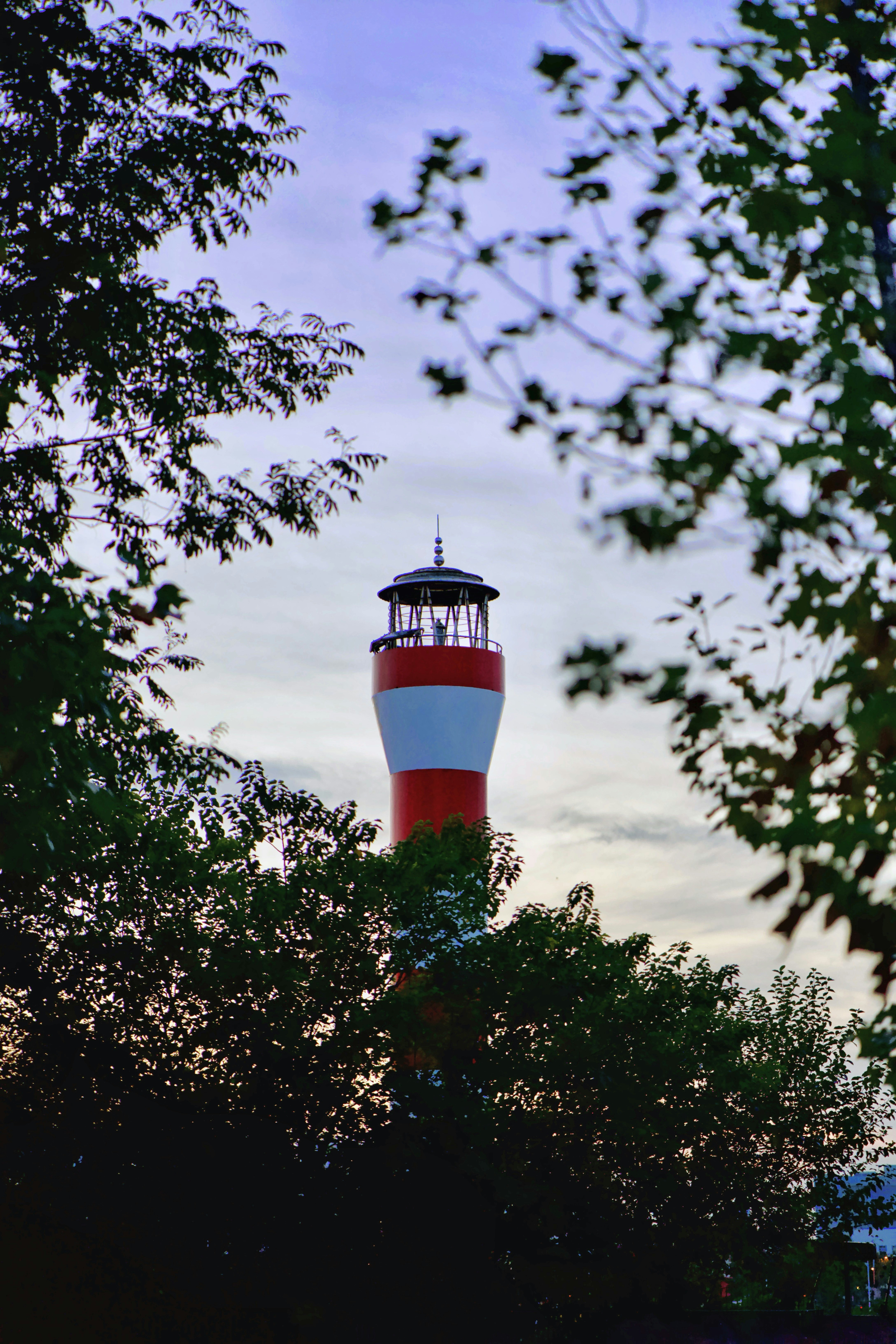 Lighthouse in a Green Frame: A Red-and-White Beacon Peeking Through Leaves
