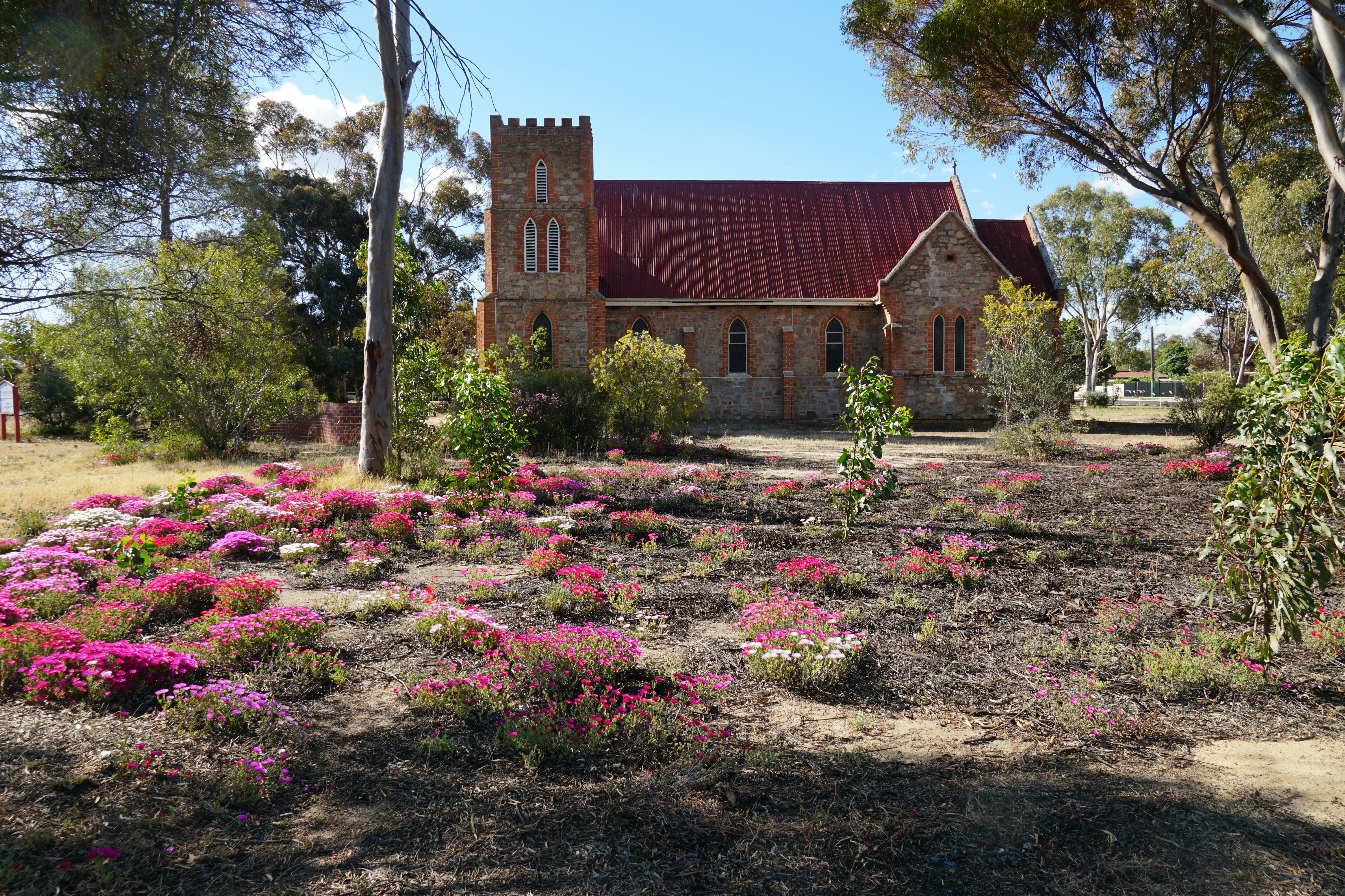 Historic stone church surrounded by vibrant pink and purple flowers in a serene landscape.