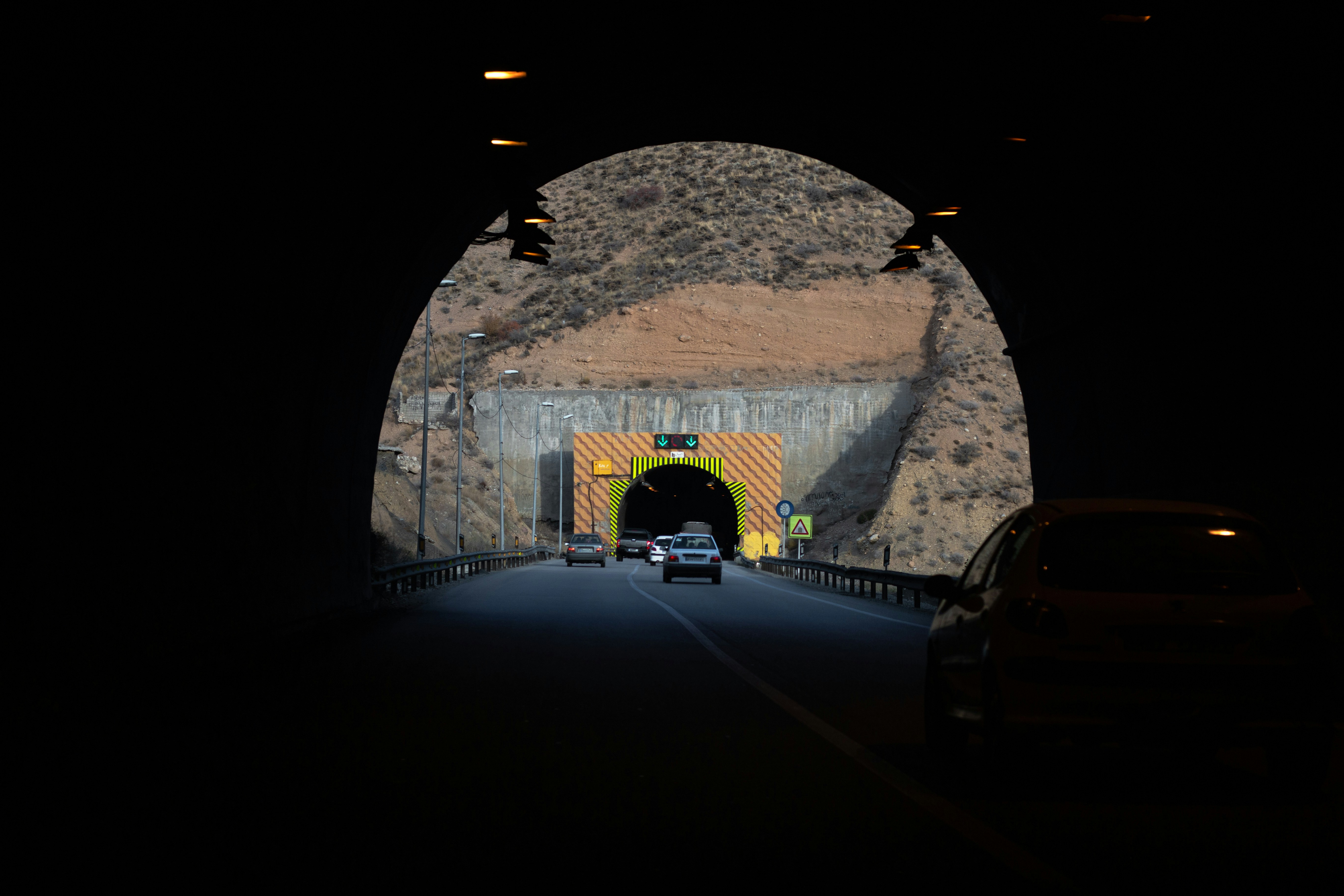 Approach to the Striped Portal: Vehicles Edge Toward the Rock-Built Tunnel