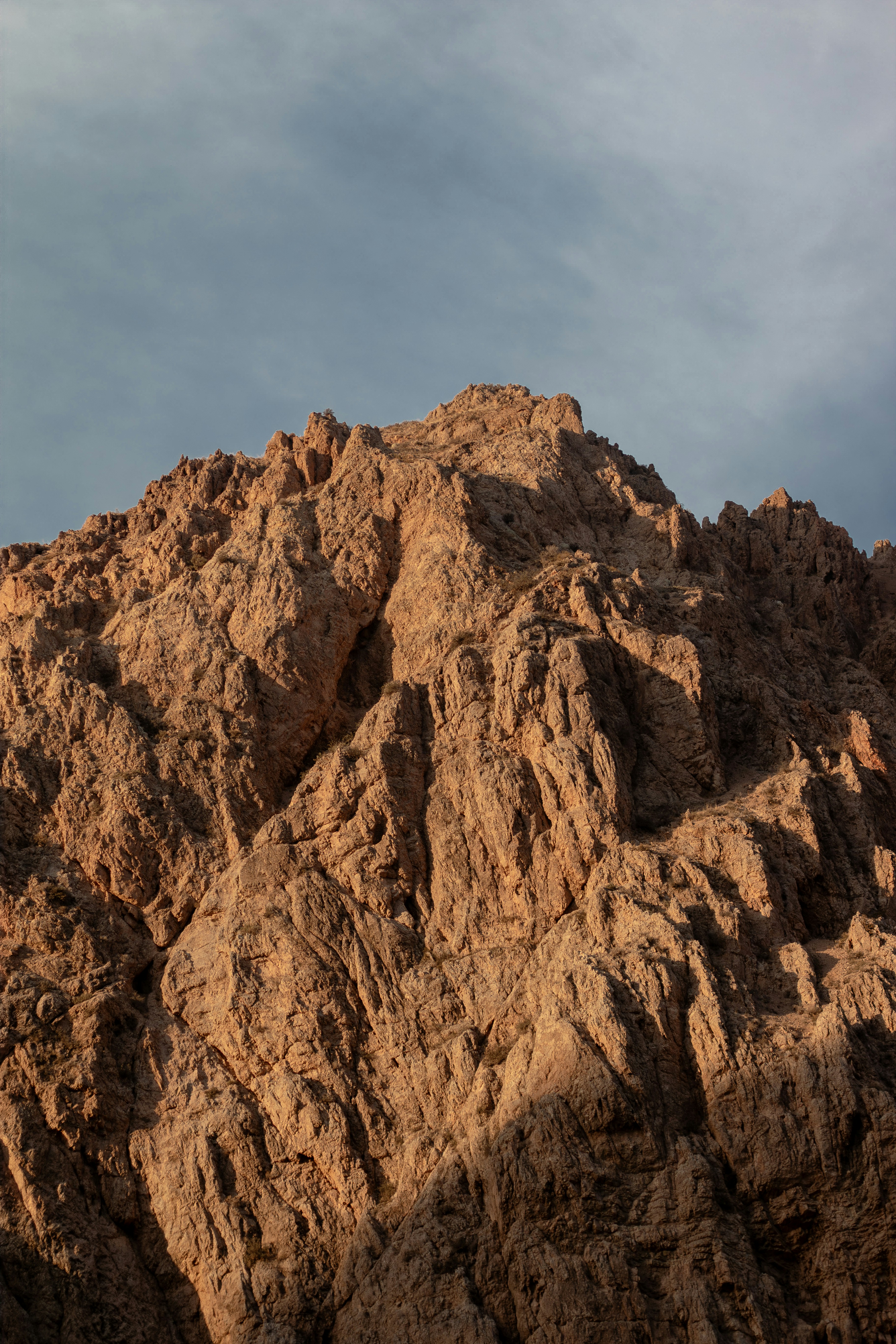 Towering mountain peak with rugged, textured rock formations under a moody sky.