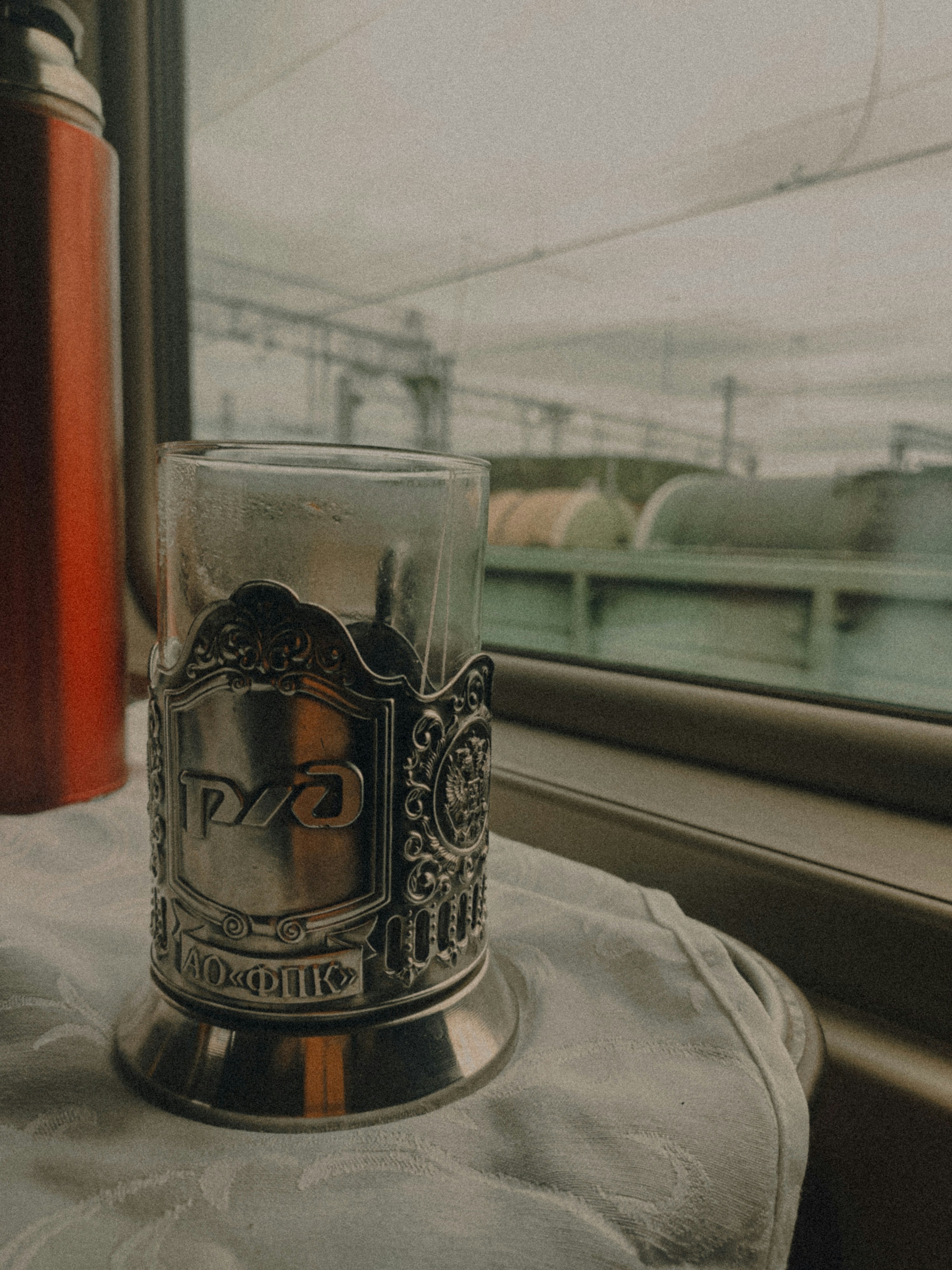 A decorative glass holder with the logo of Russian Railways rests on a table, with a blurred view of the passing landscape through the train window.