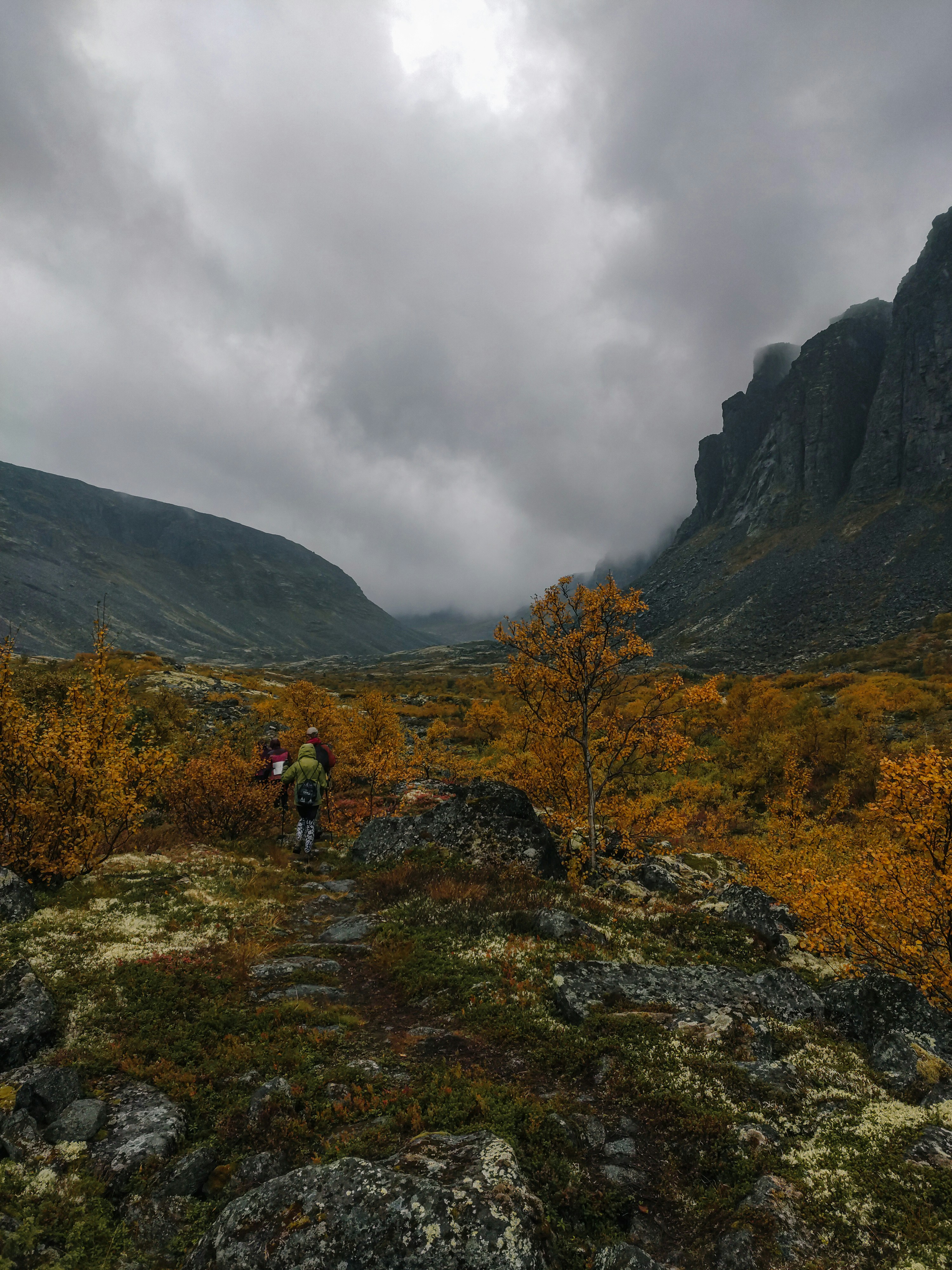 Autumn Ascent: Hikers Amid Fiery Dales Beneath a Stormy Veil