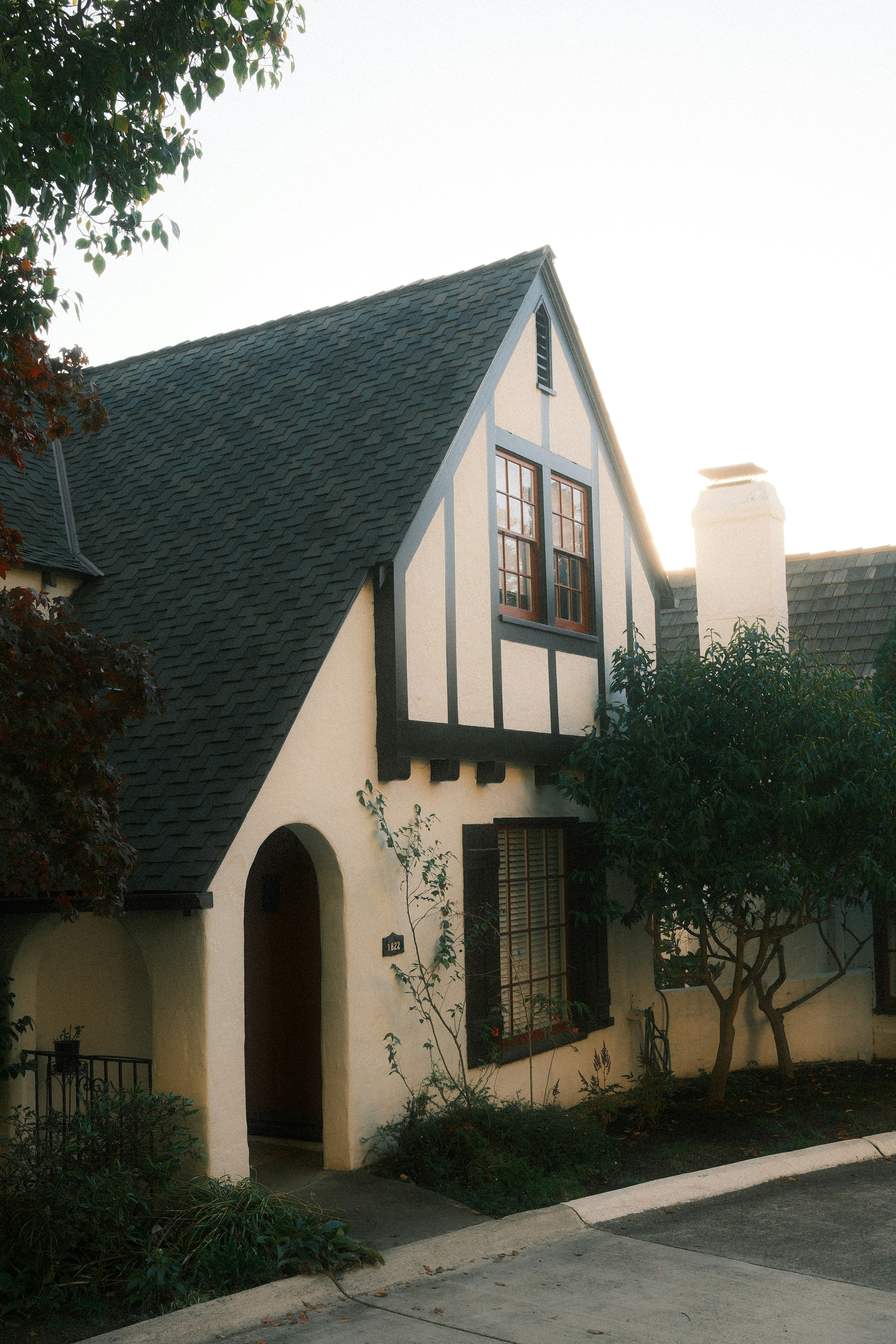Tudor-style house featuring intricate gables, decorative half-timbering, and lush greenery in the foreground.