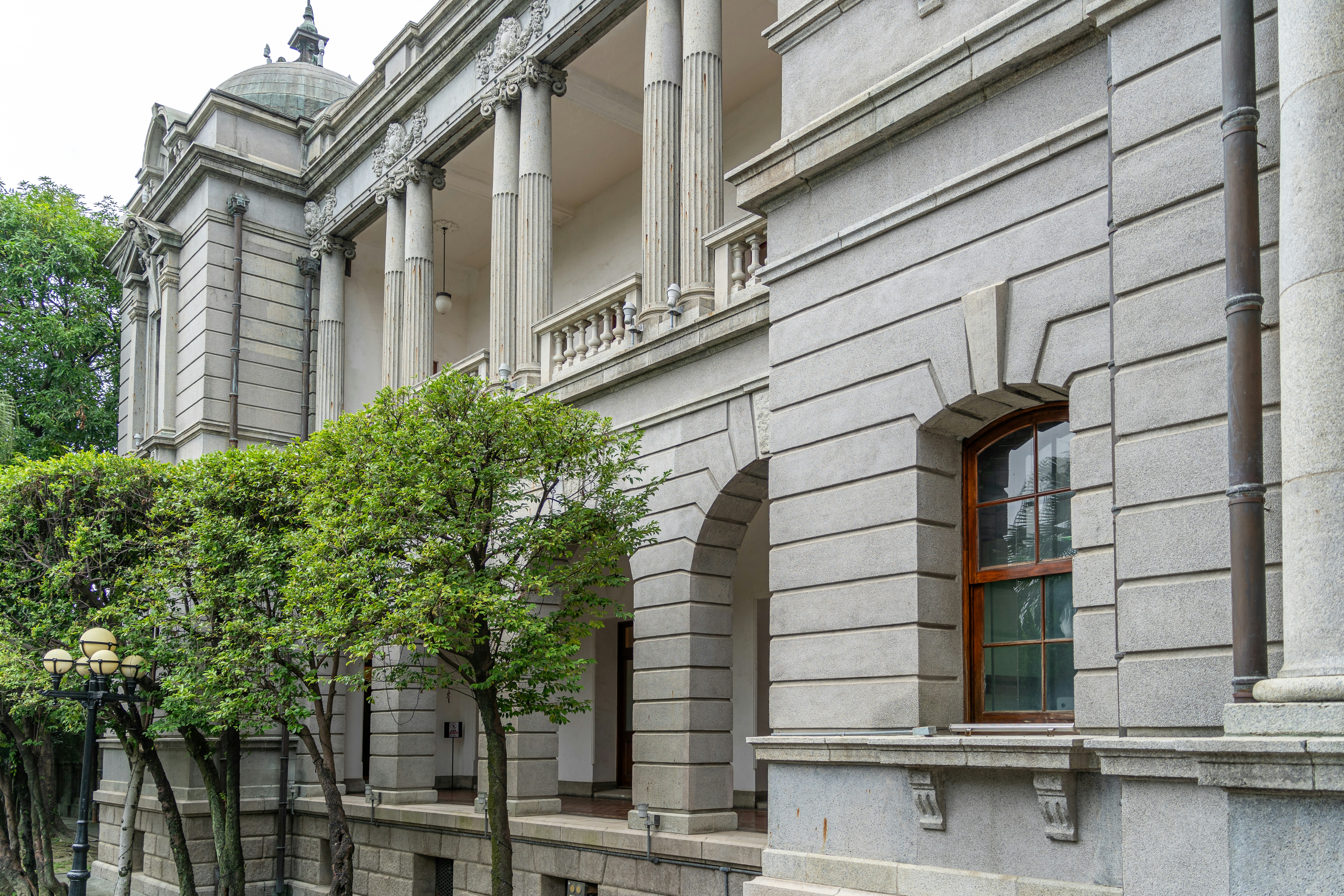 Historic building facade showcasing classical architecture, framed by lush greenery and soft lighting.
