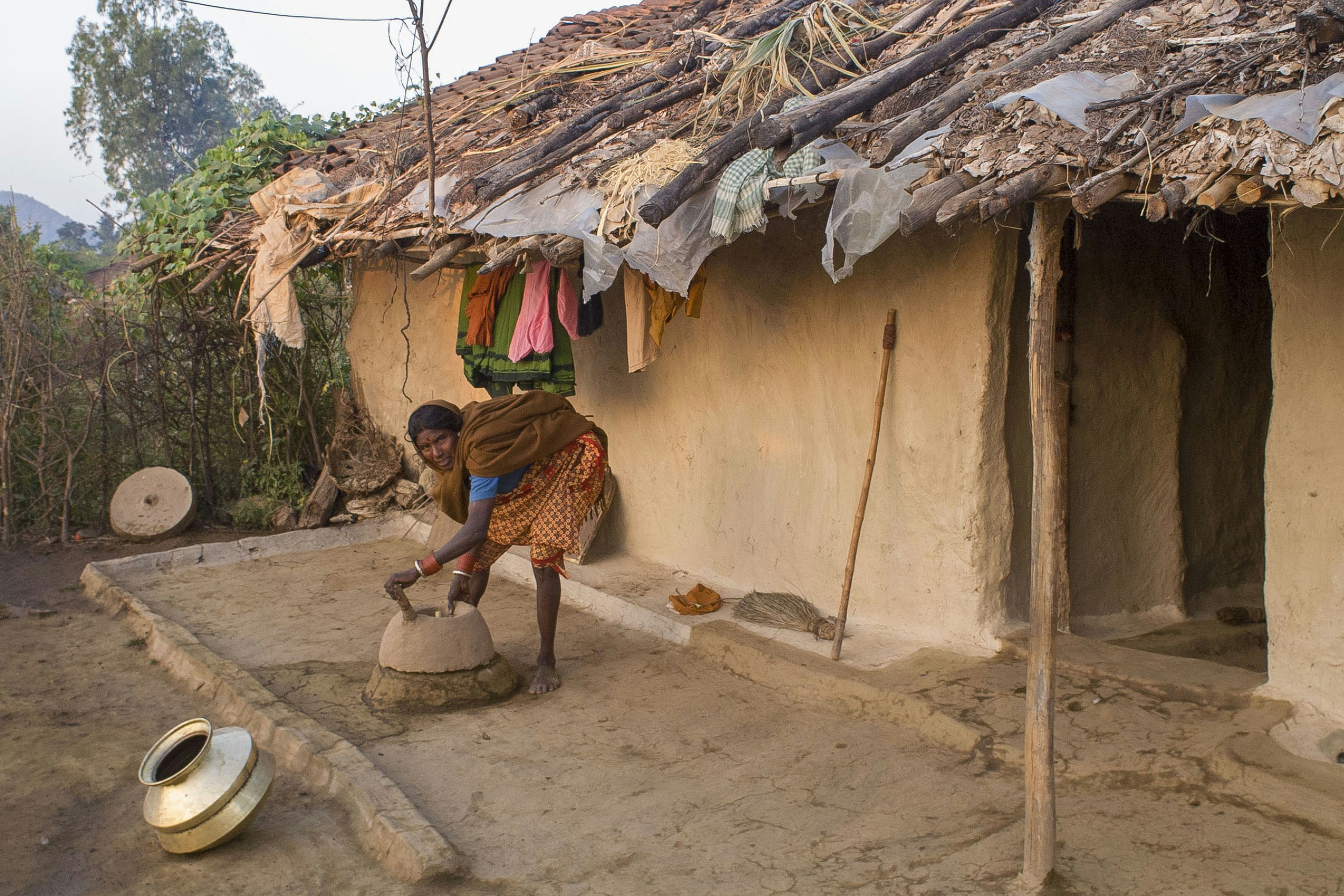 A woman skillfully shaping clay pottery outside a rustic home, surrounded by nature and traditional architecture.