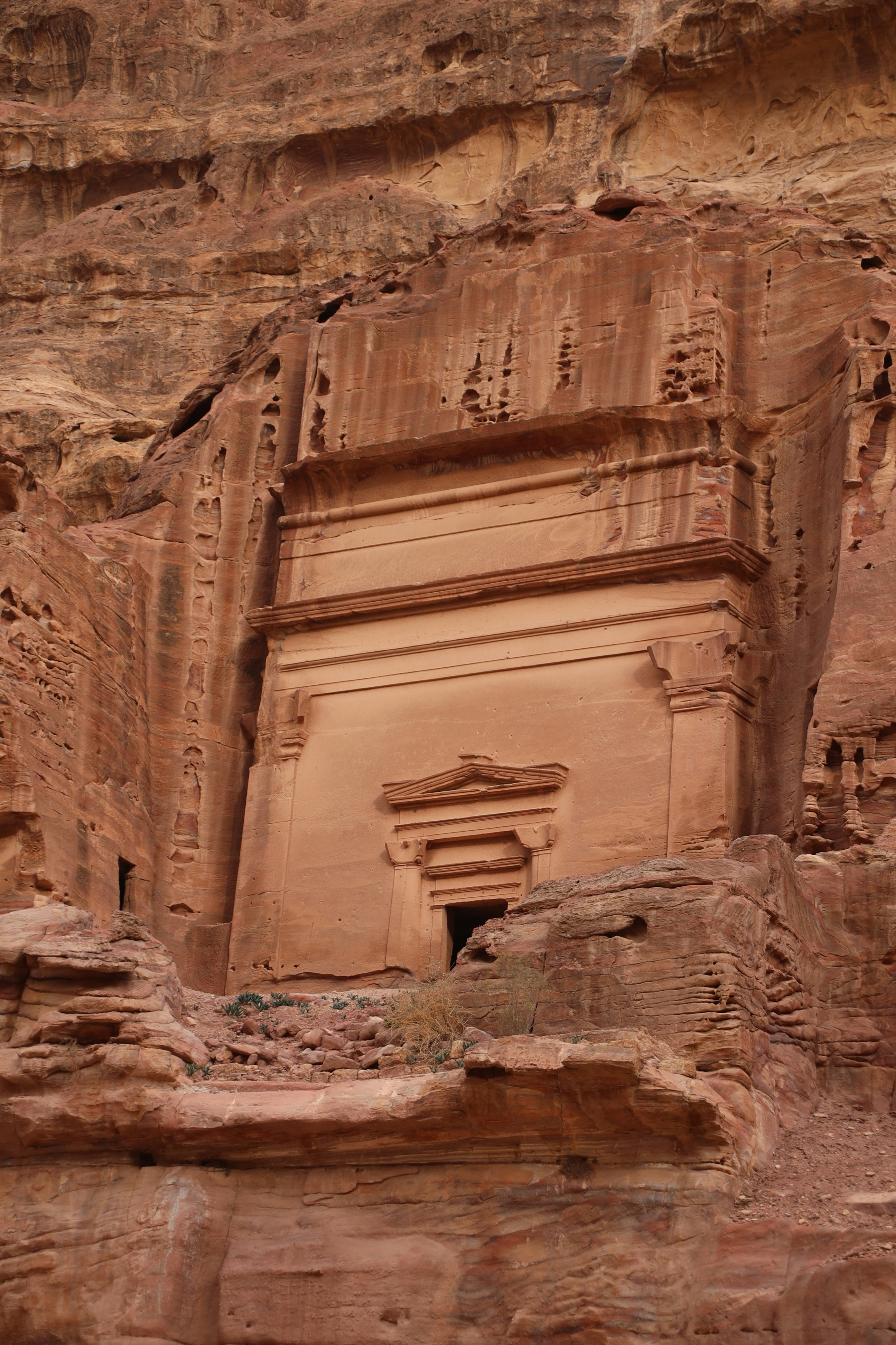 Intricate facade of a rock-cut tomb nestled within towering sandstone cliffs, showcasing ancient architectural artistry.