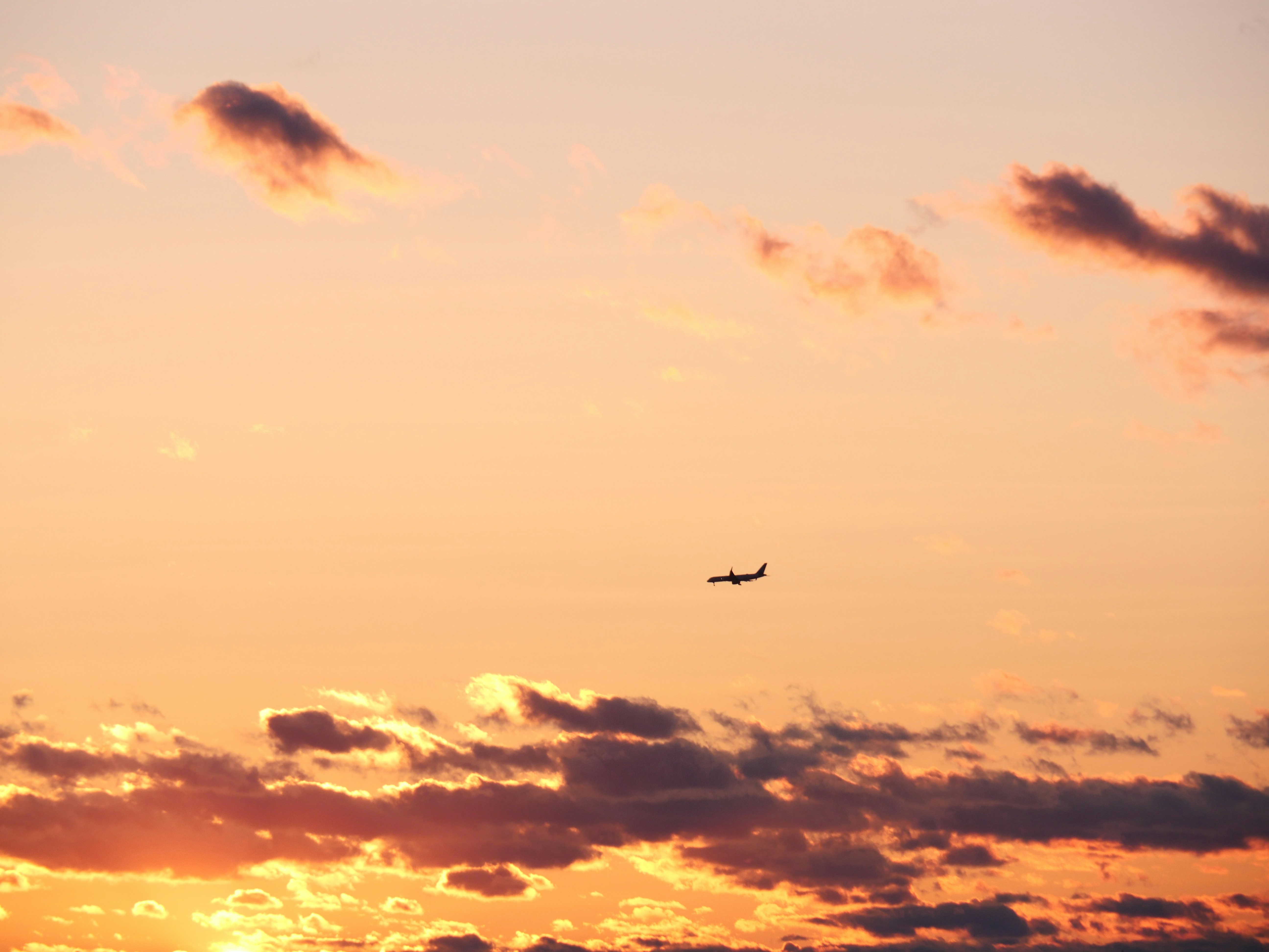 Airplane silhouetted against a vibrant sunset sky filled with soft clouds and warm hues.