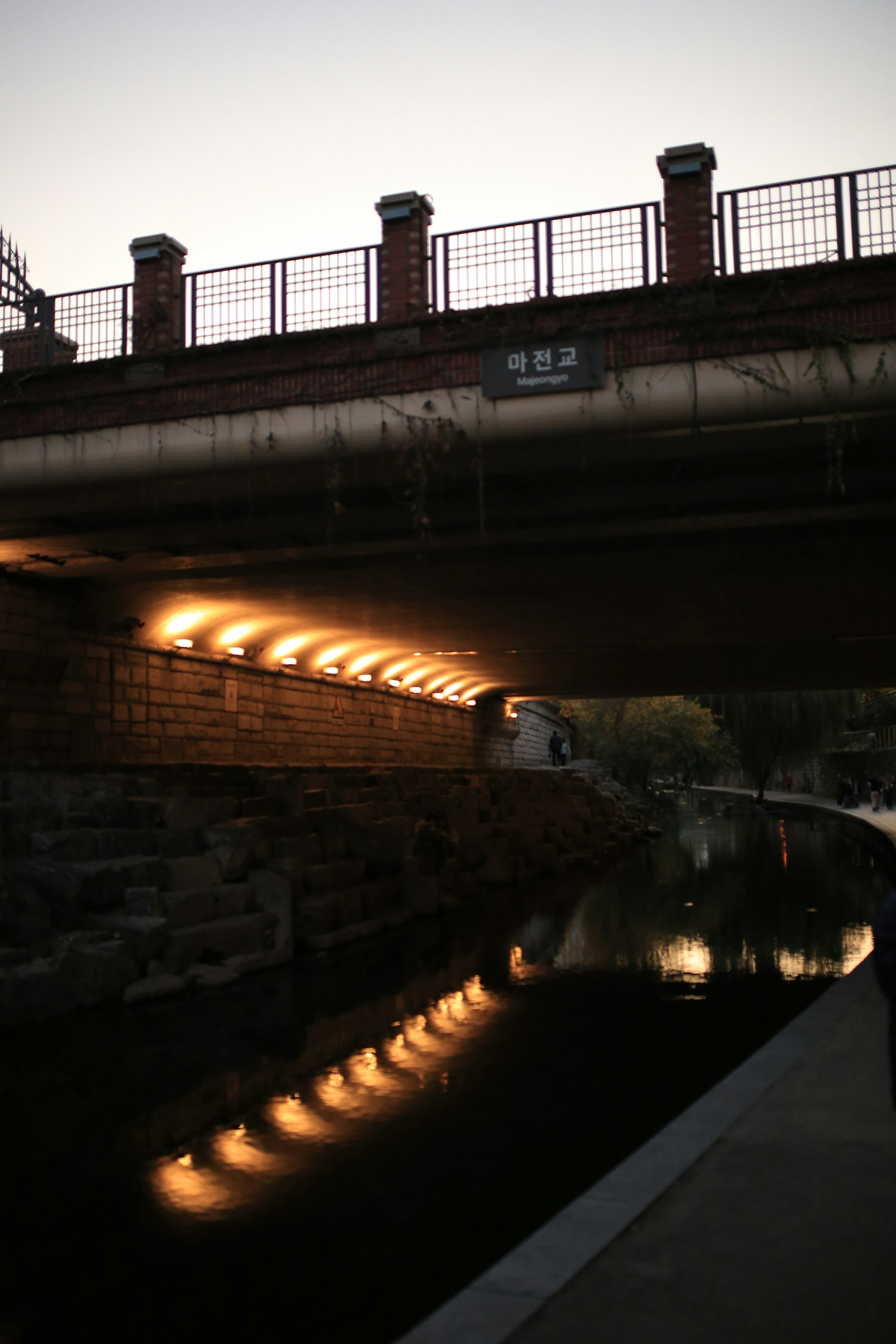 Softly illuminated underpass with reflections on the water's surface, creating a serene atmosphere at dusk.