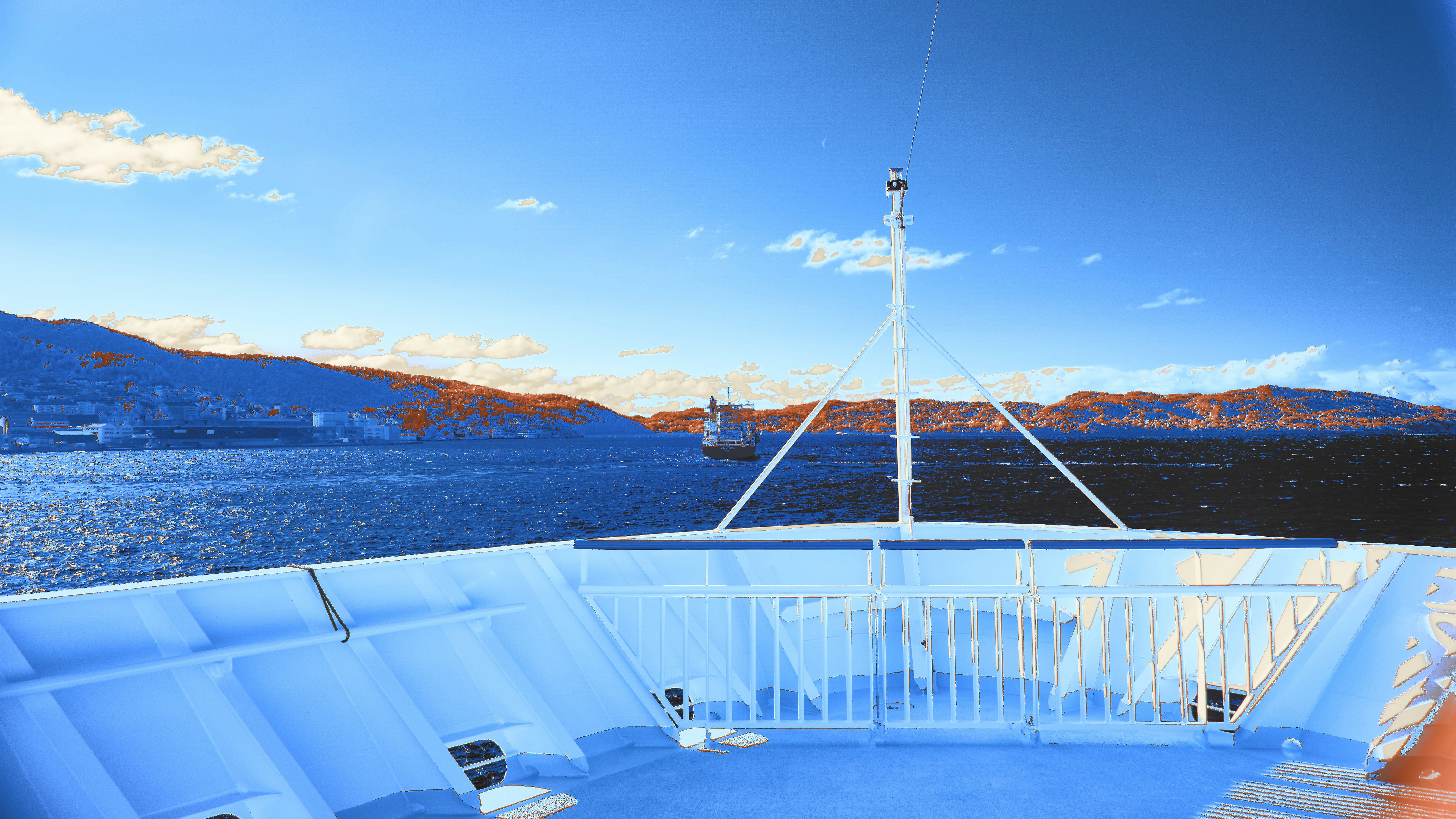 View from the bow of a boat, showcasing a vibrant blue sea and distant mountains under a bright sky.