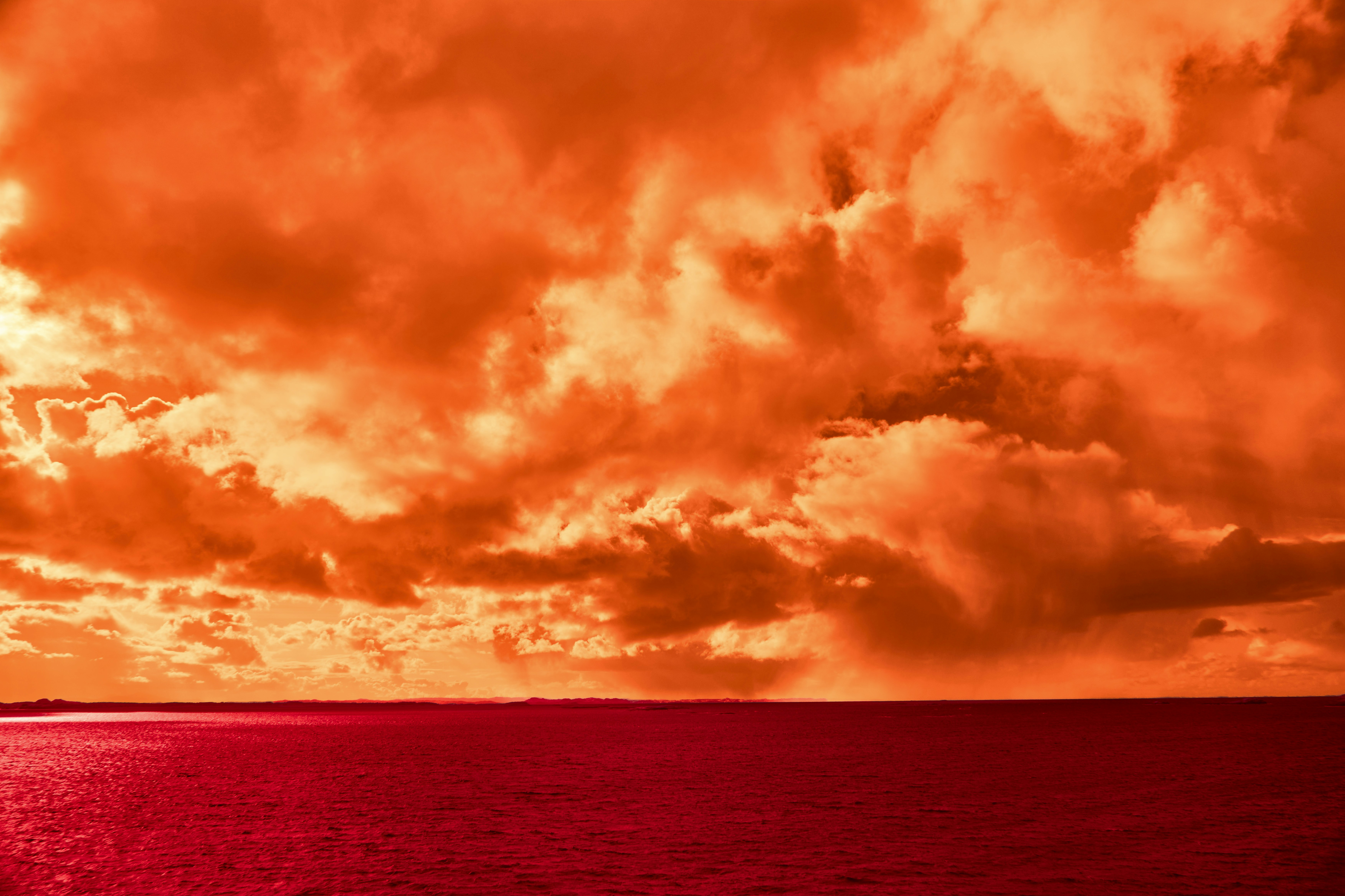Vibrant orange clouds reflecting on a tranquil ocean surface during sunset. The dramatic interplay of colors creates a surreal atmosphere.