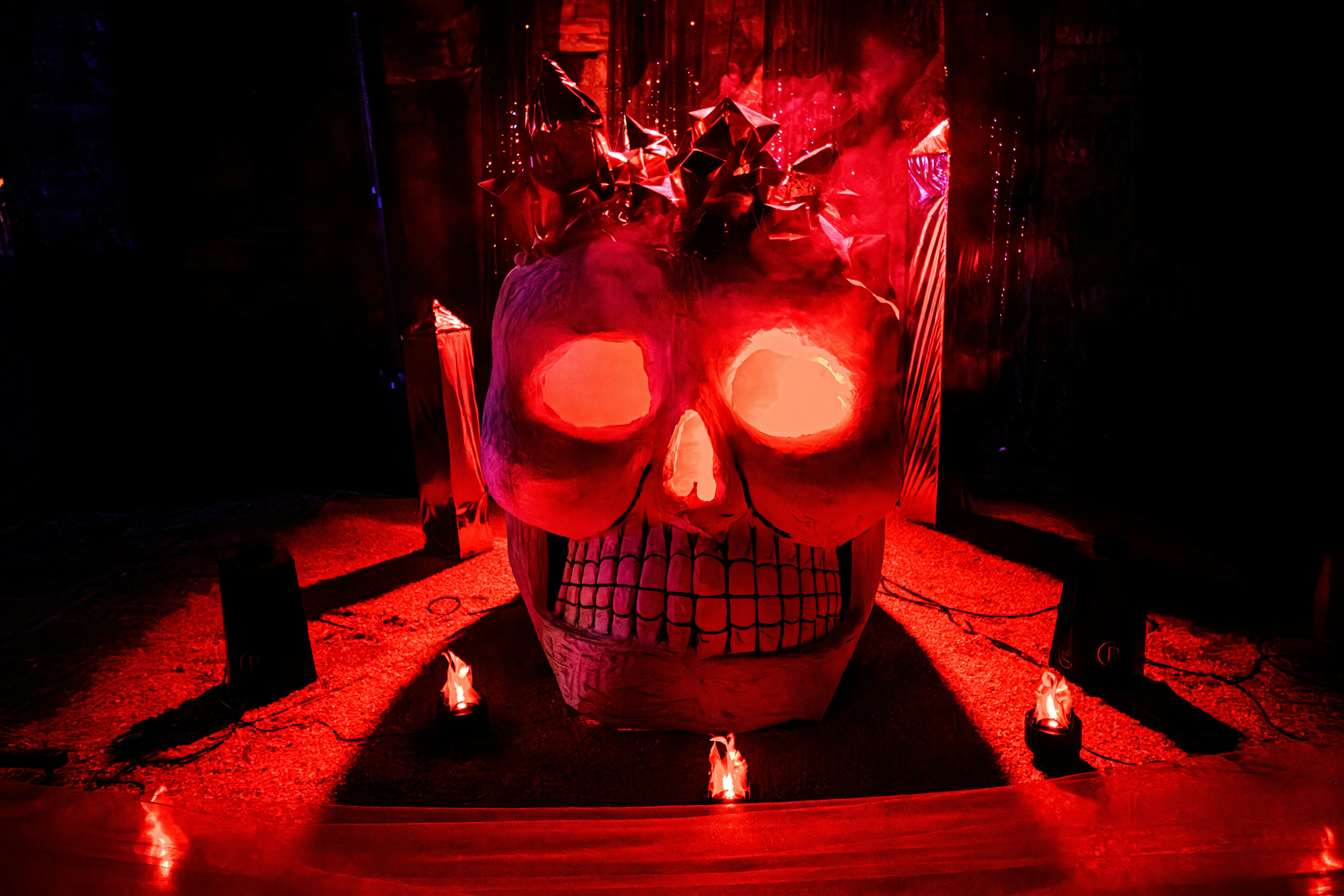 Giant skull centerpiece adorned with spikes, glowing red eyes, surrounded by candles in a darkened setting.