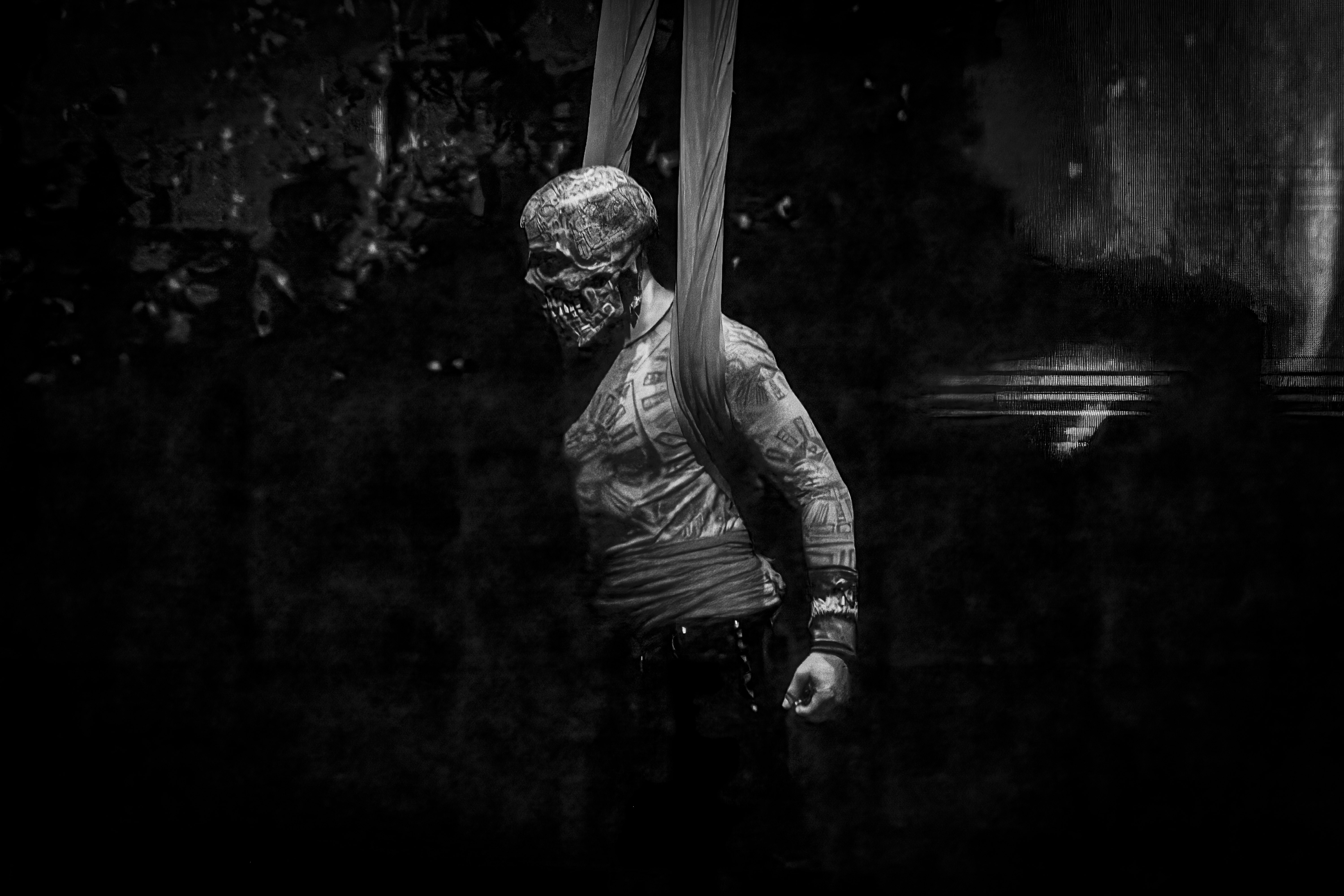 A tattooed figure with a skull mask hangs suspended, embodying themes of struggle and defiance against a dark backdrop.