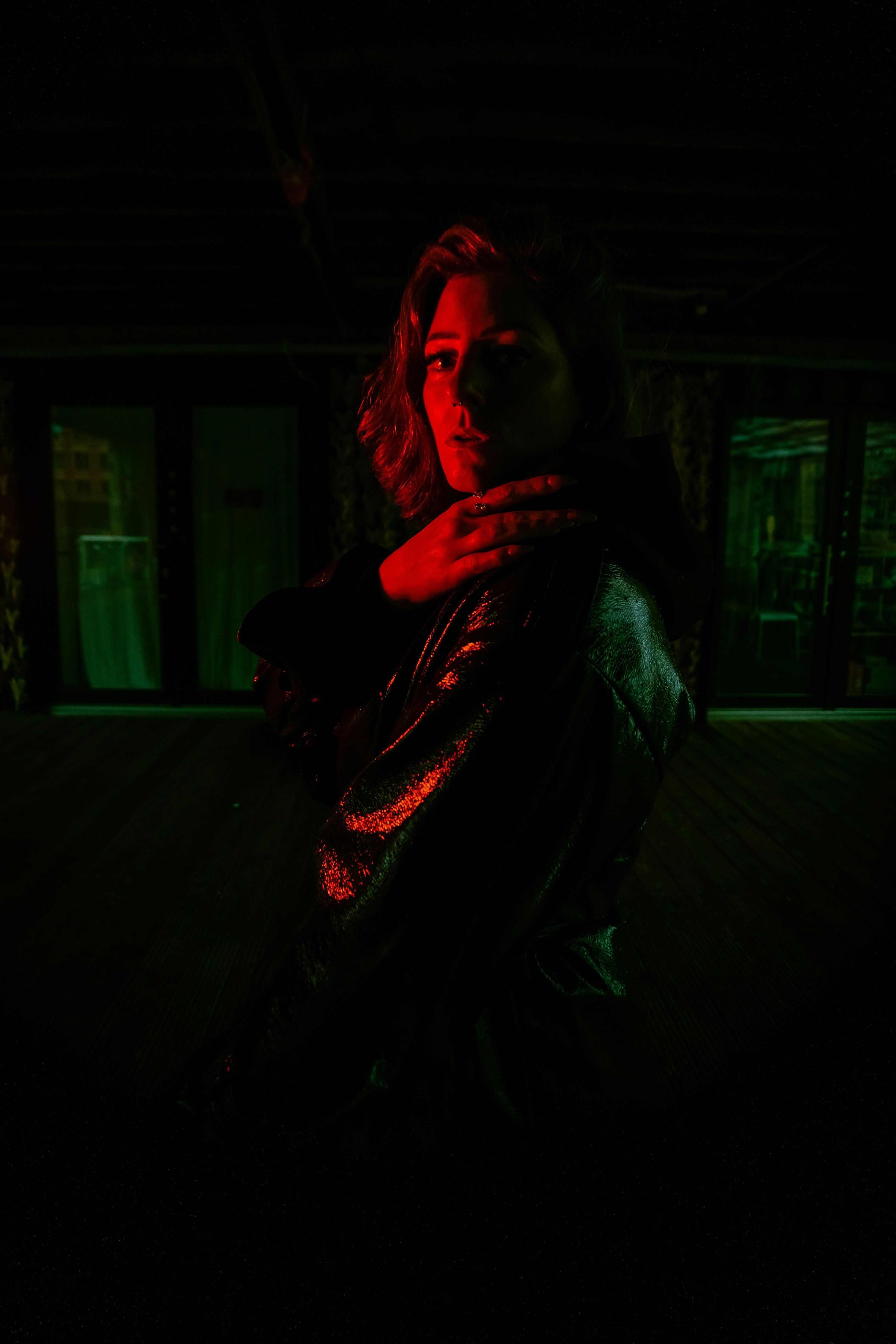 Model in a reflective jacket poses dramatically against a darkened backdrop illuminated by red and green lights.