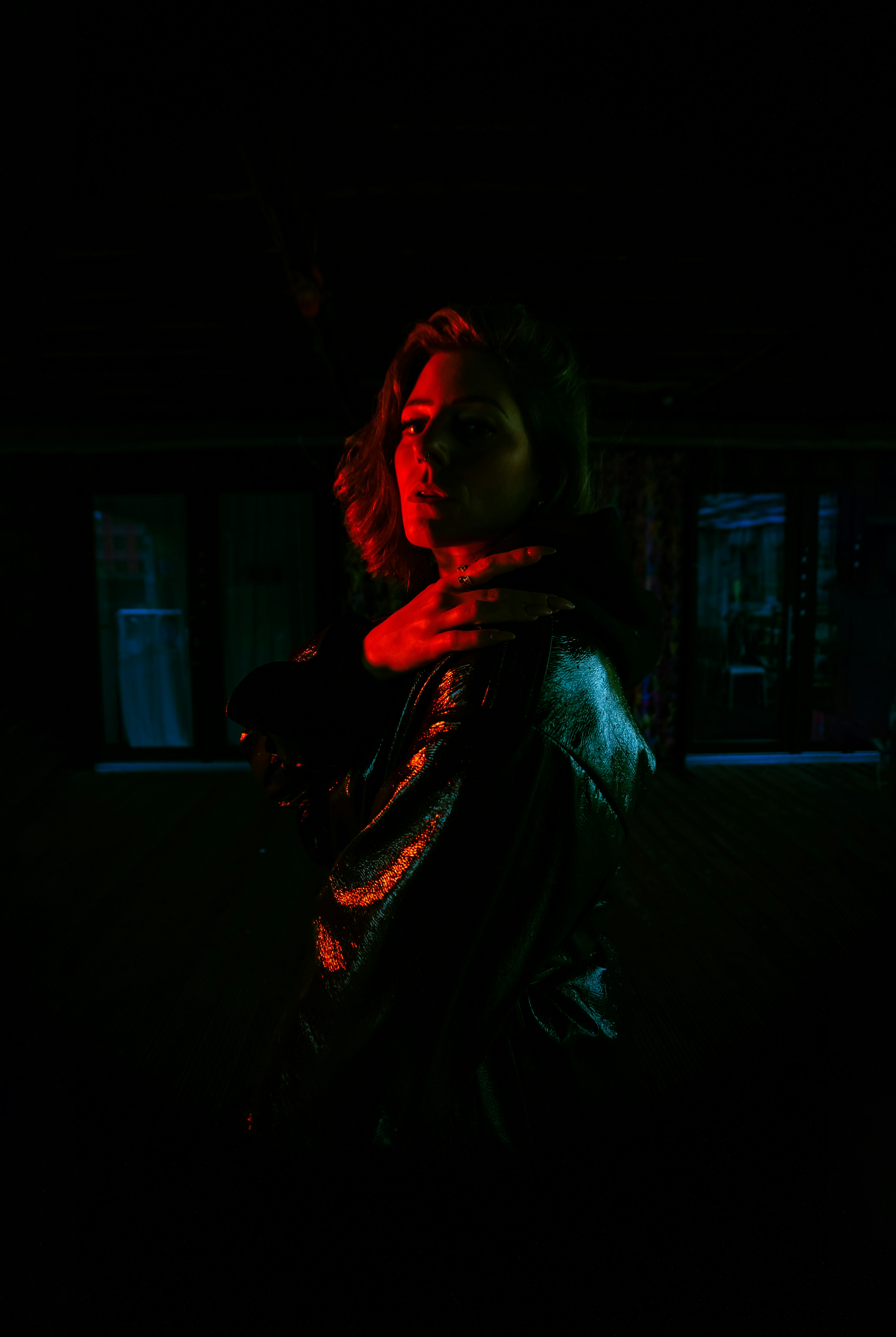 A figure in a reflective jacket stands against a dark background, illuminated by contrasting red and blue lights, creating a dramatic atmosphere.