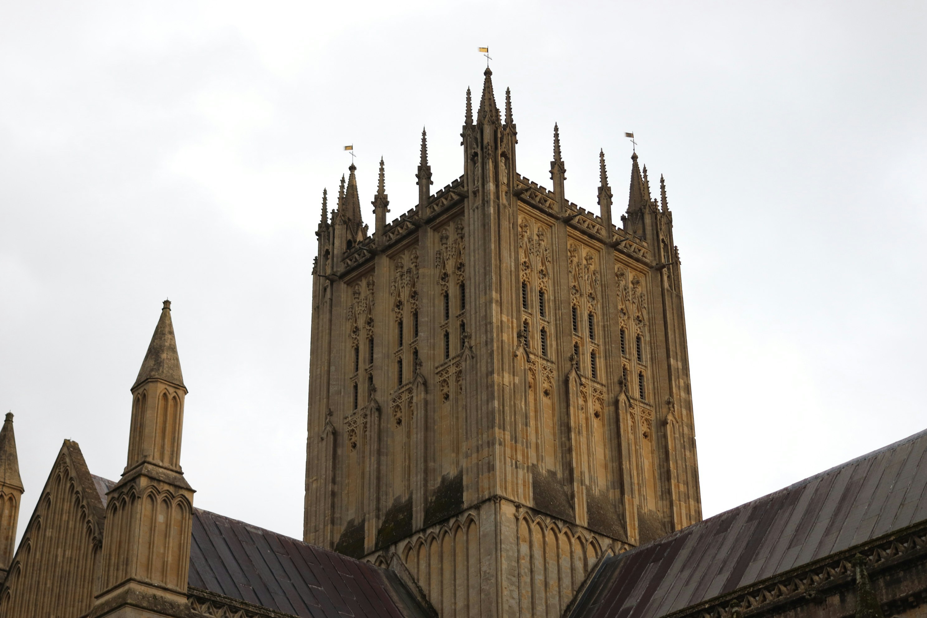 Imposing cathedral tower rises majestically, showcasing intricate stonework and pointed spires under a cloudy sky.