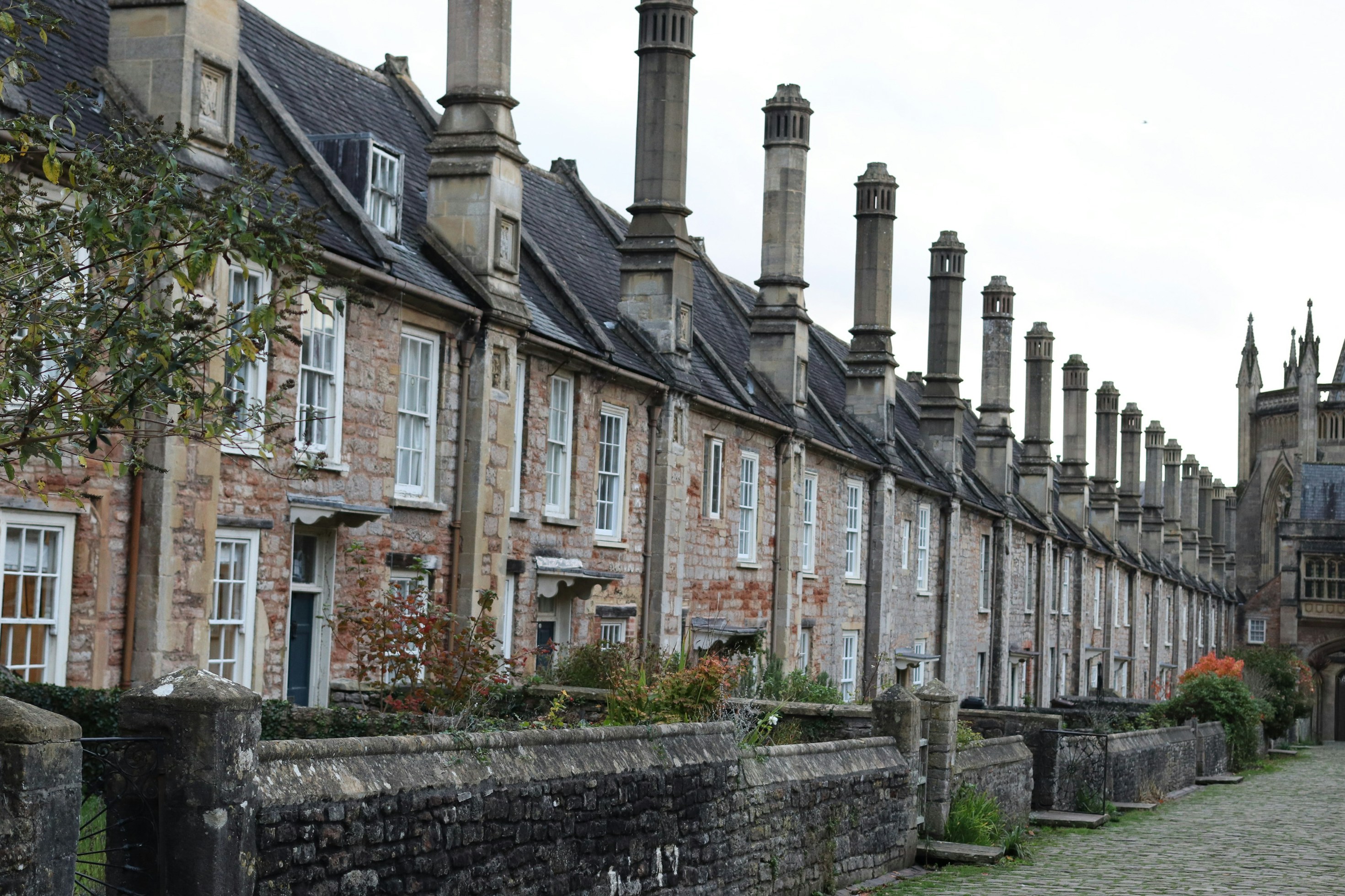 Row of historic houses showcasing unique chimney designs and stone walls, framed by a cobblestone path and greenery.