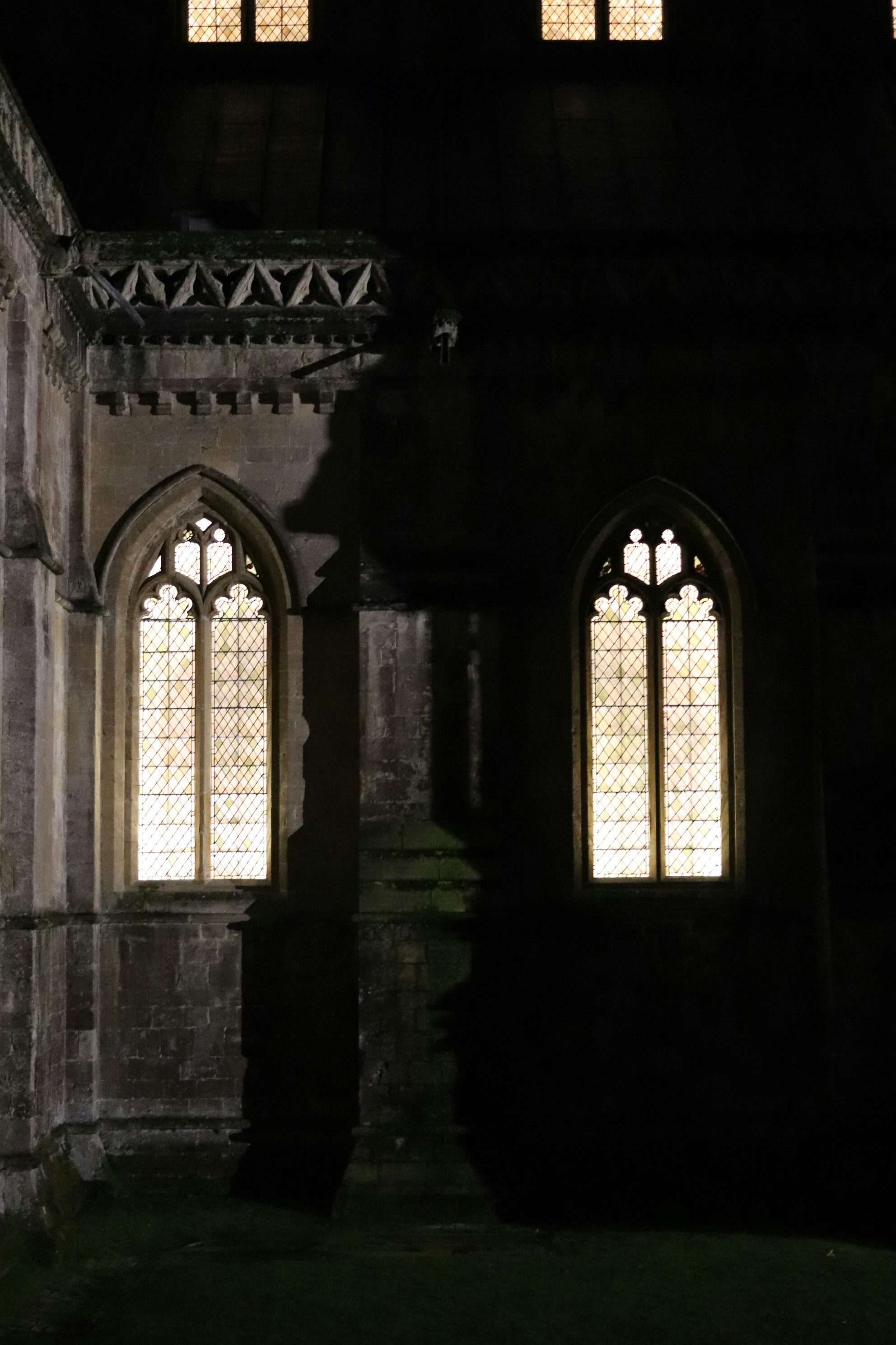 Gothic architecture featuring two illuminated stained glass windows against a dark stone backdrop, creating a dramatic contrast.