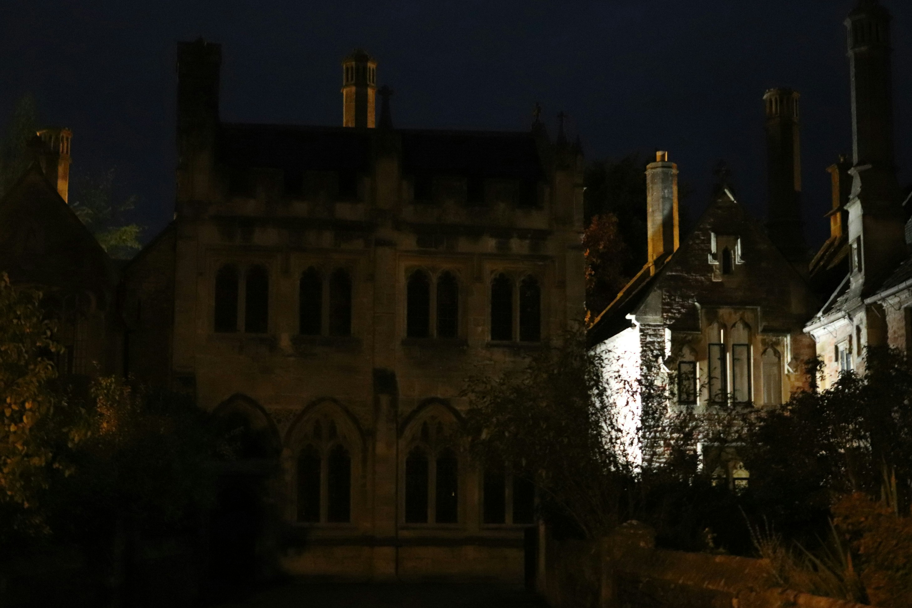 Gothic-style buildings shrouded in darkness, with one structure illuminated by a soft light, creating a mysterious atmosphere.