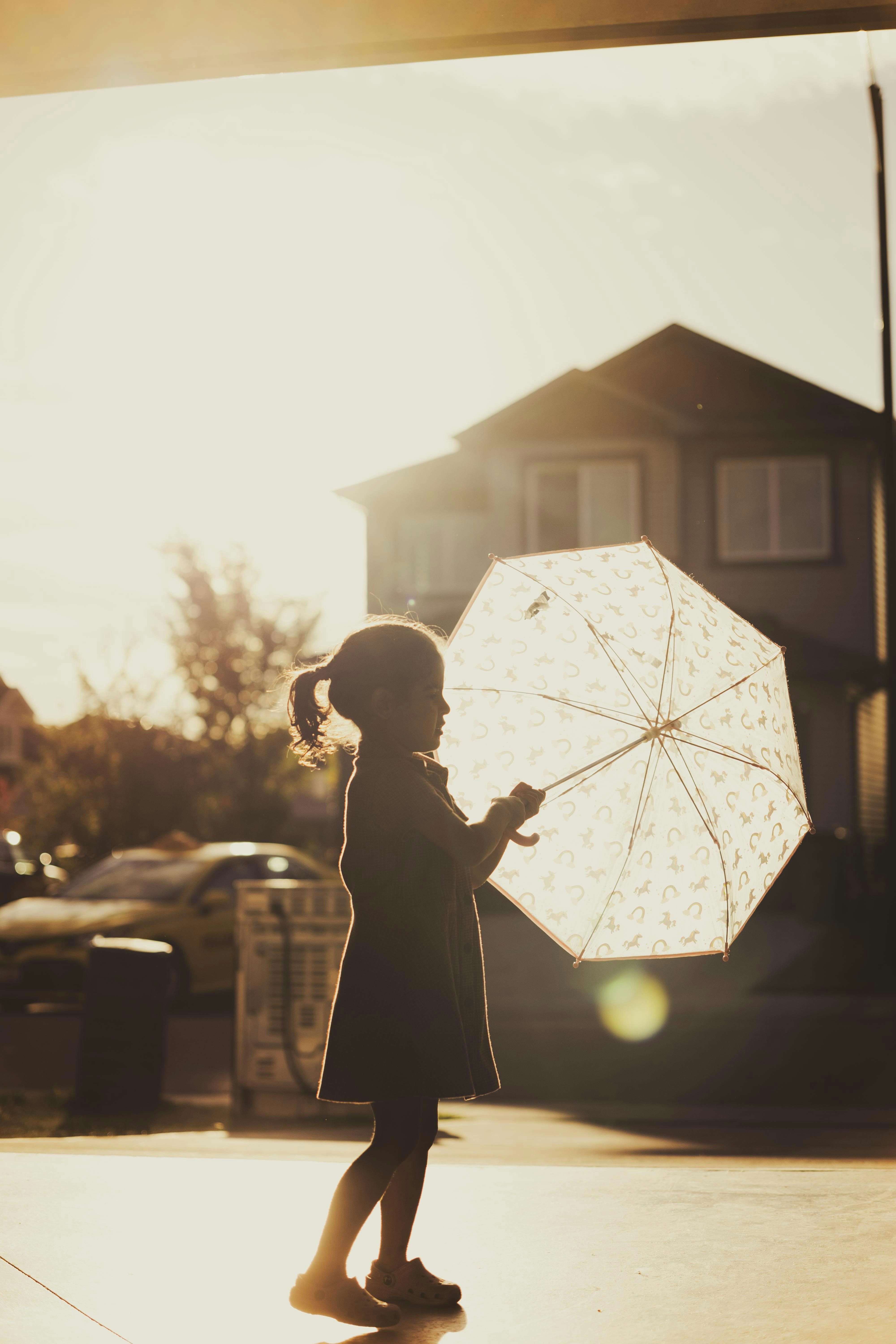 Golden Hour Silhouette: A Girl with a Patterned Umbrella in a Quiet Suburban Driveway