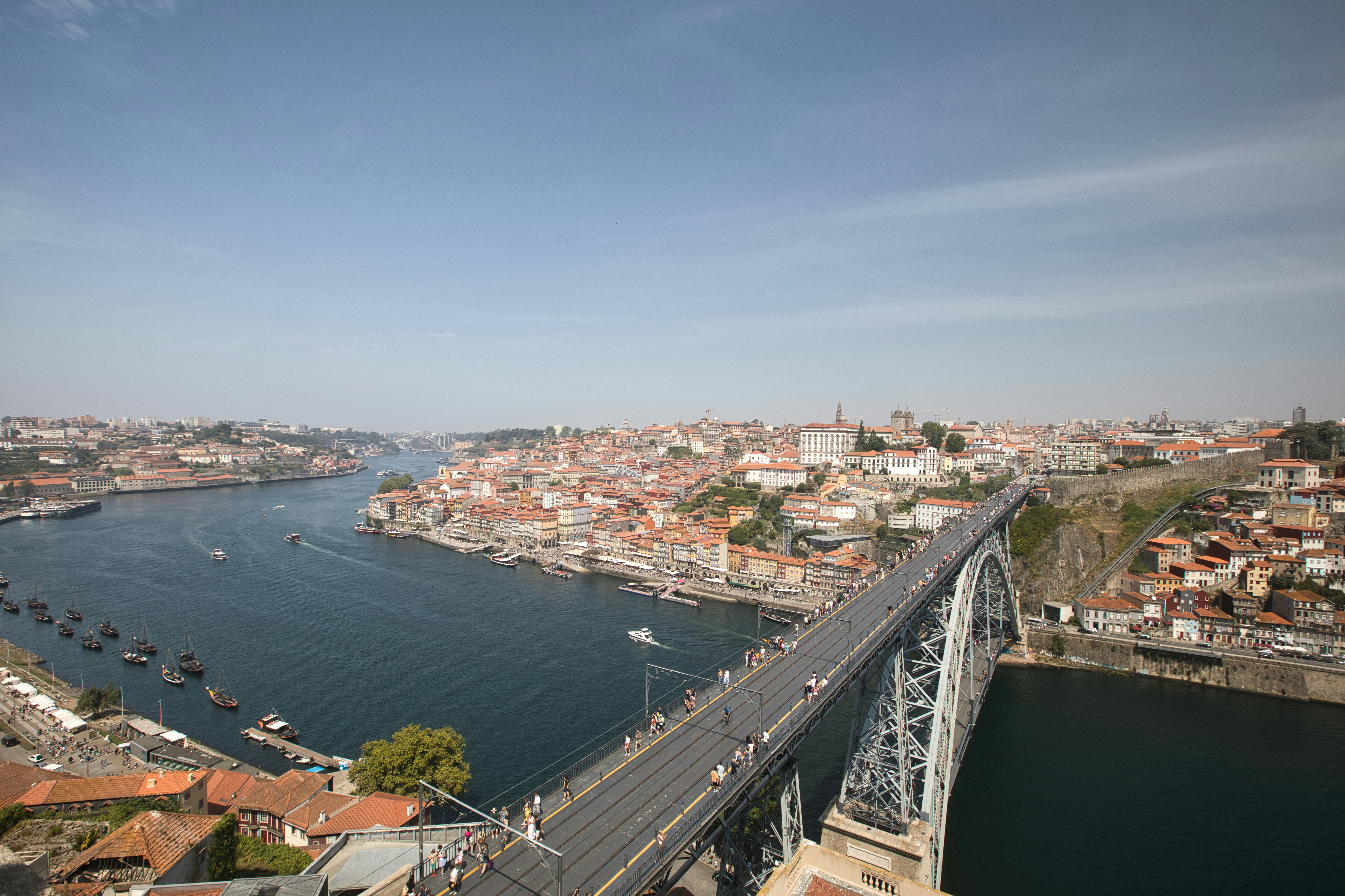 A panoramic view showcasing the iconic bridge spanning the river, with colorful buildings lining the banks of Porto. The scene captures the lively atmosphere of the city.
