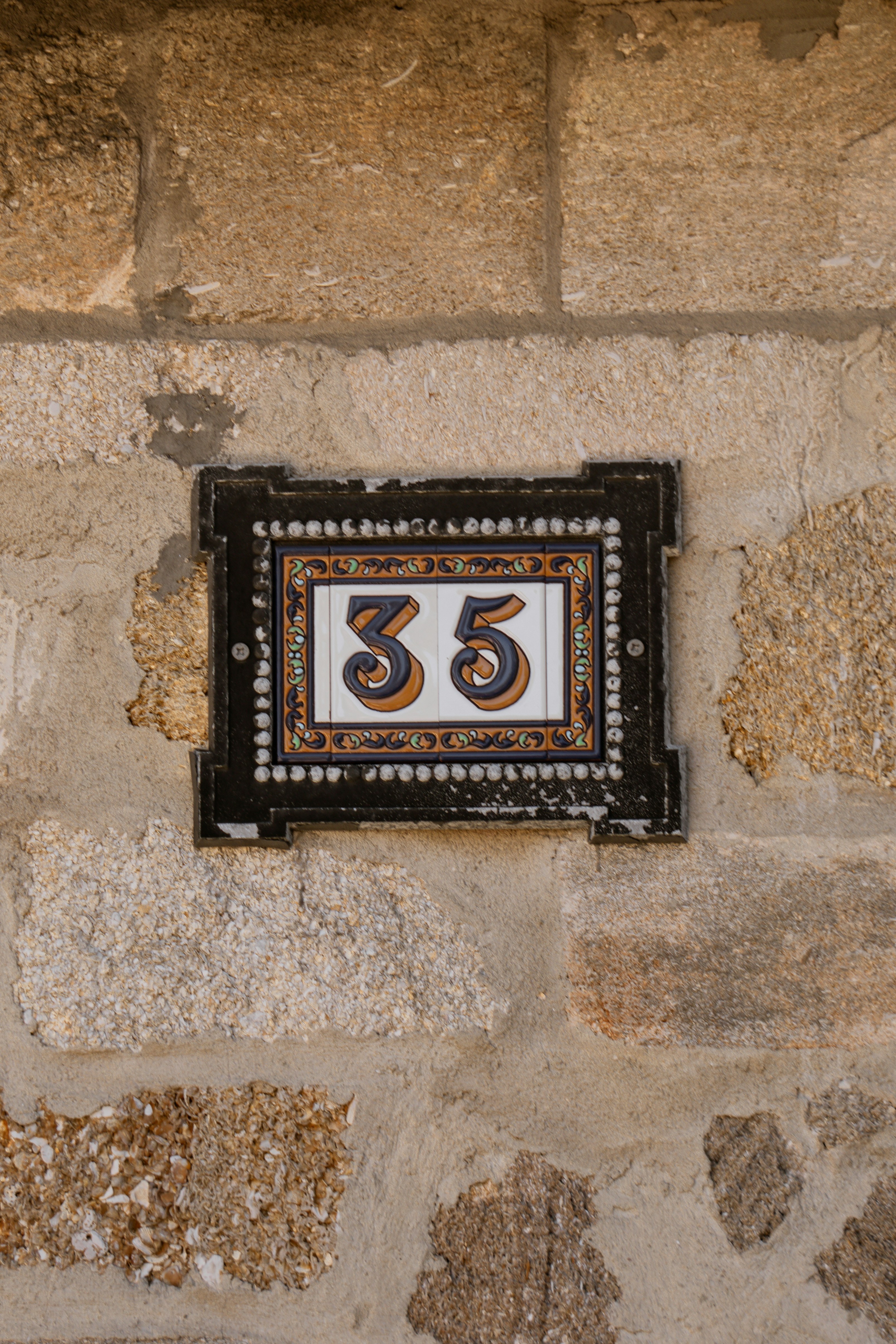 Decorative house number '35' framed by rustic stone wall, showcasing intricate tile work and texture contrast.