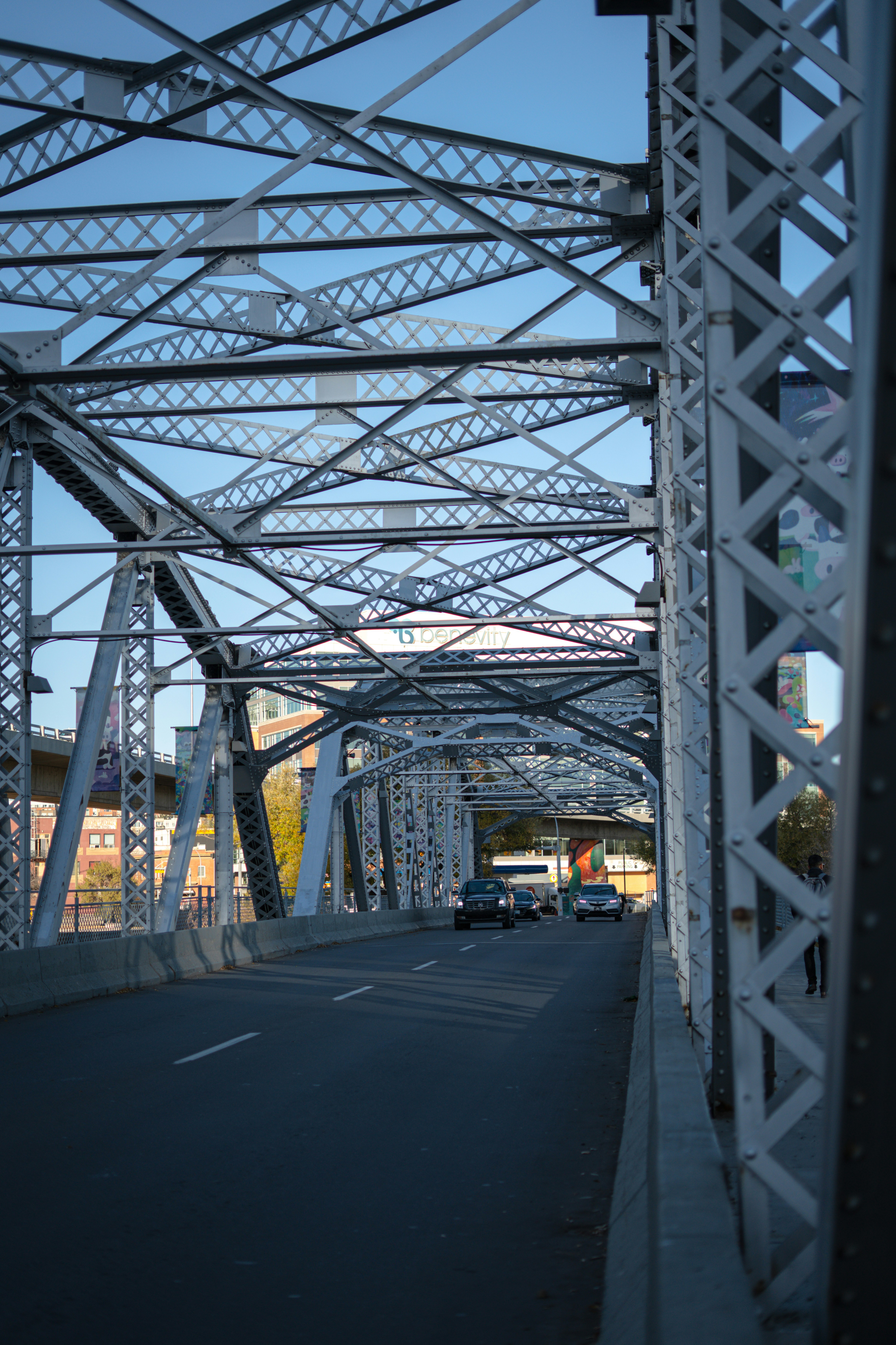 Intricate steel framework of a bridge framing a busy roadway beneath a clear blue sky.