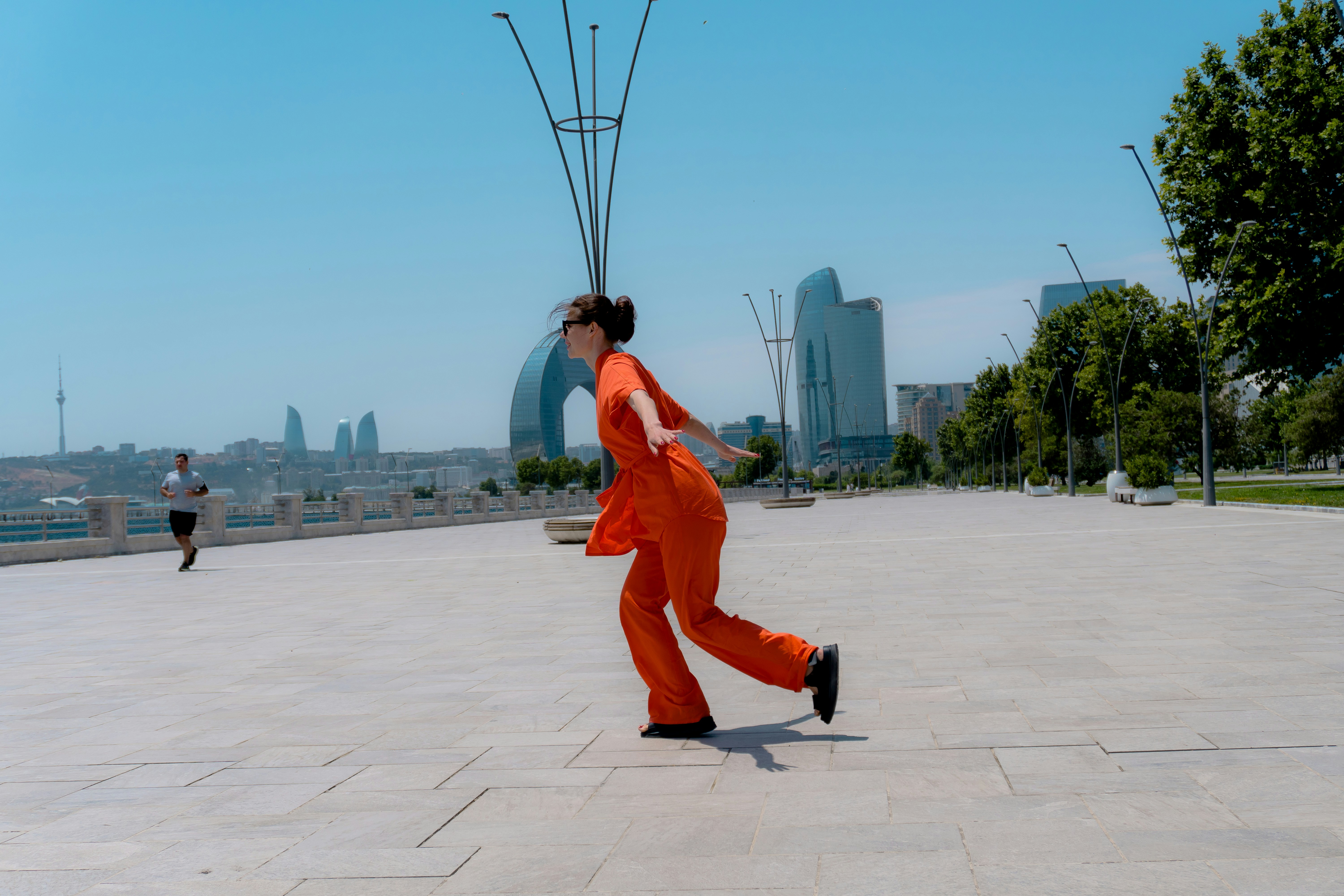 Woman in orange dancing in a city park.