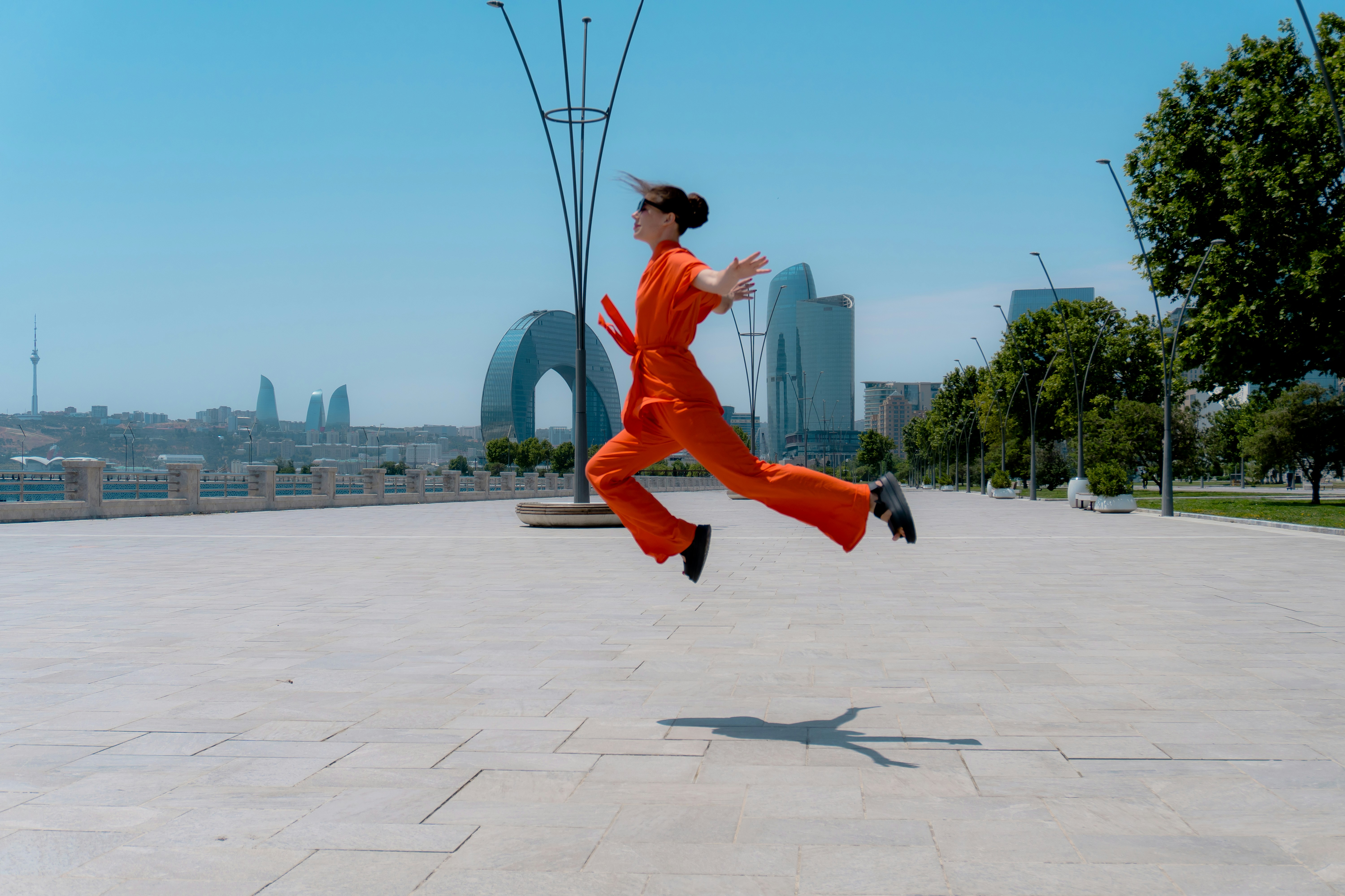 A dancer in an orange jumpsuit leaps gracefully against a backdrop of modern architecture, showcasing a vibrant urban landscape.