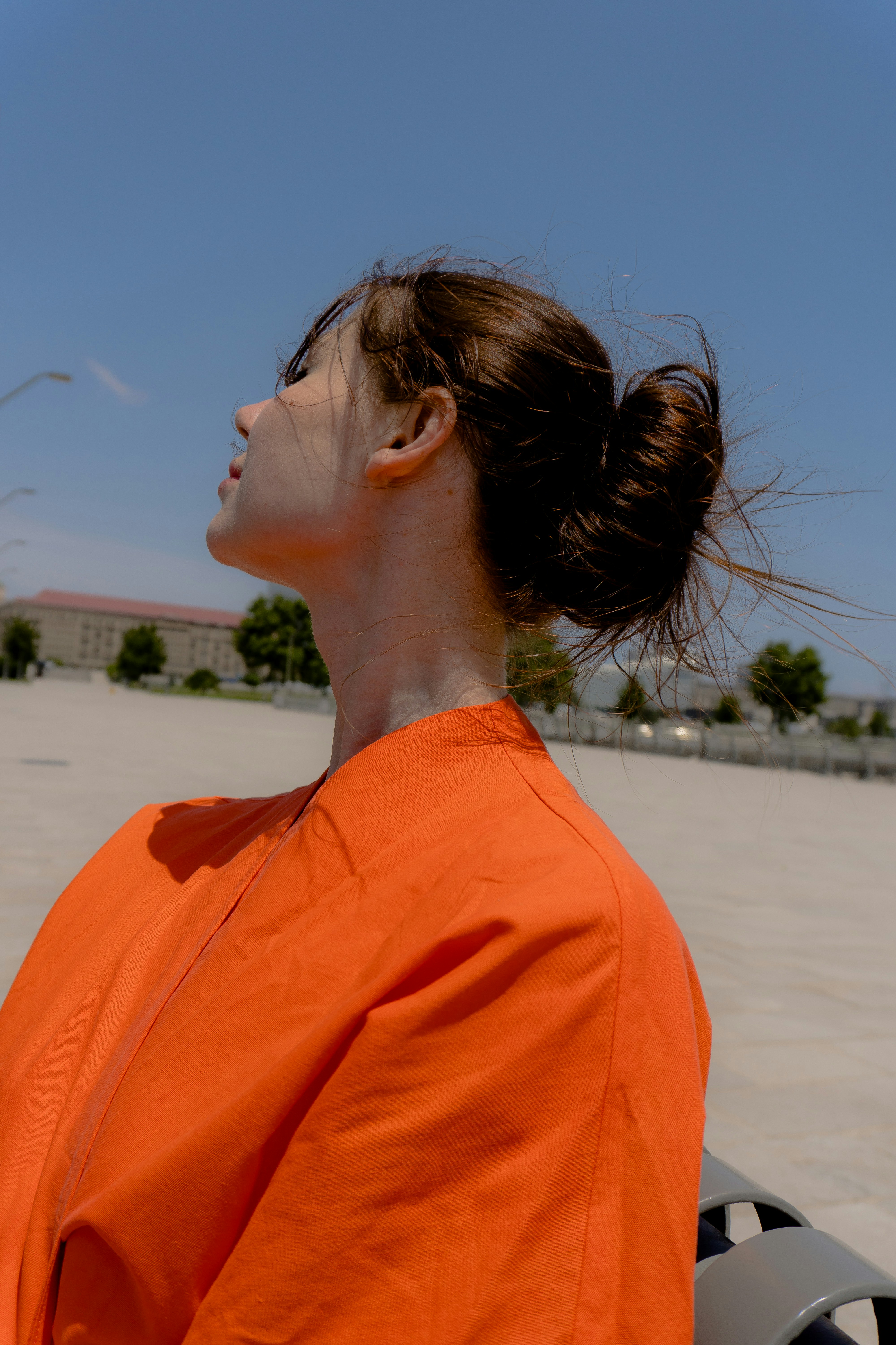 Orange Garment, Open Sky: A Quiet Profile on a Sunlit Plaza