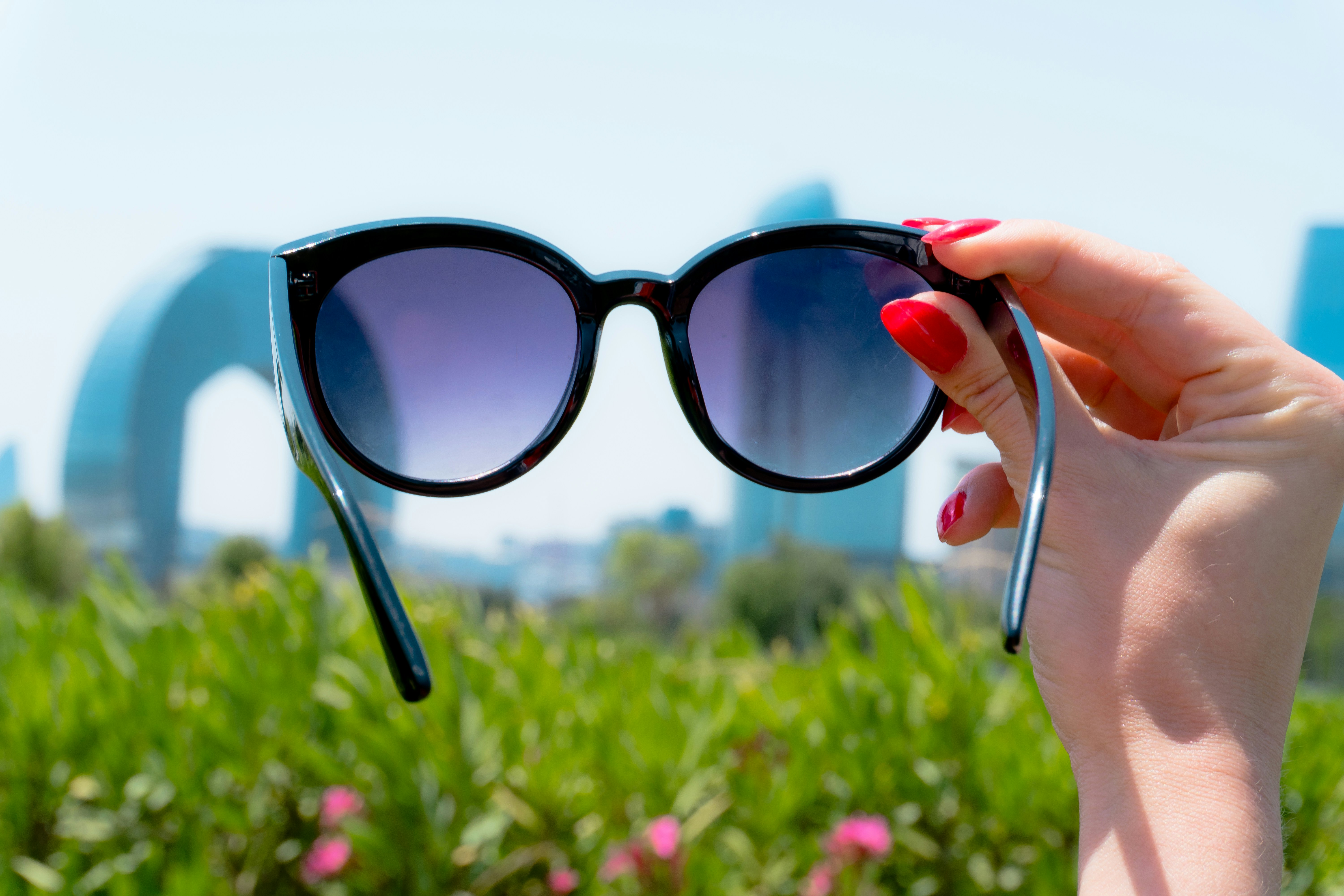 Frame in Focus: Sunglasses Held Against a Sunlit City Garden Backdrop
