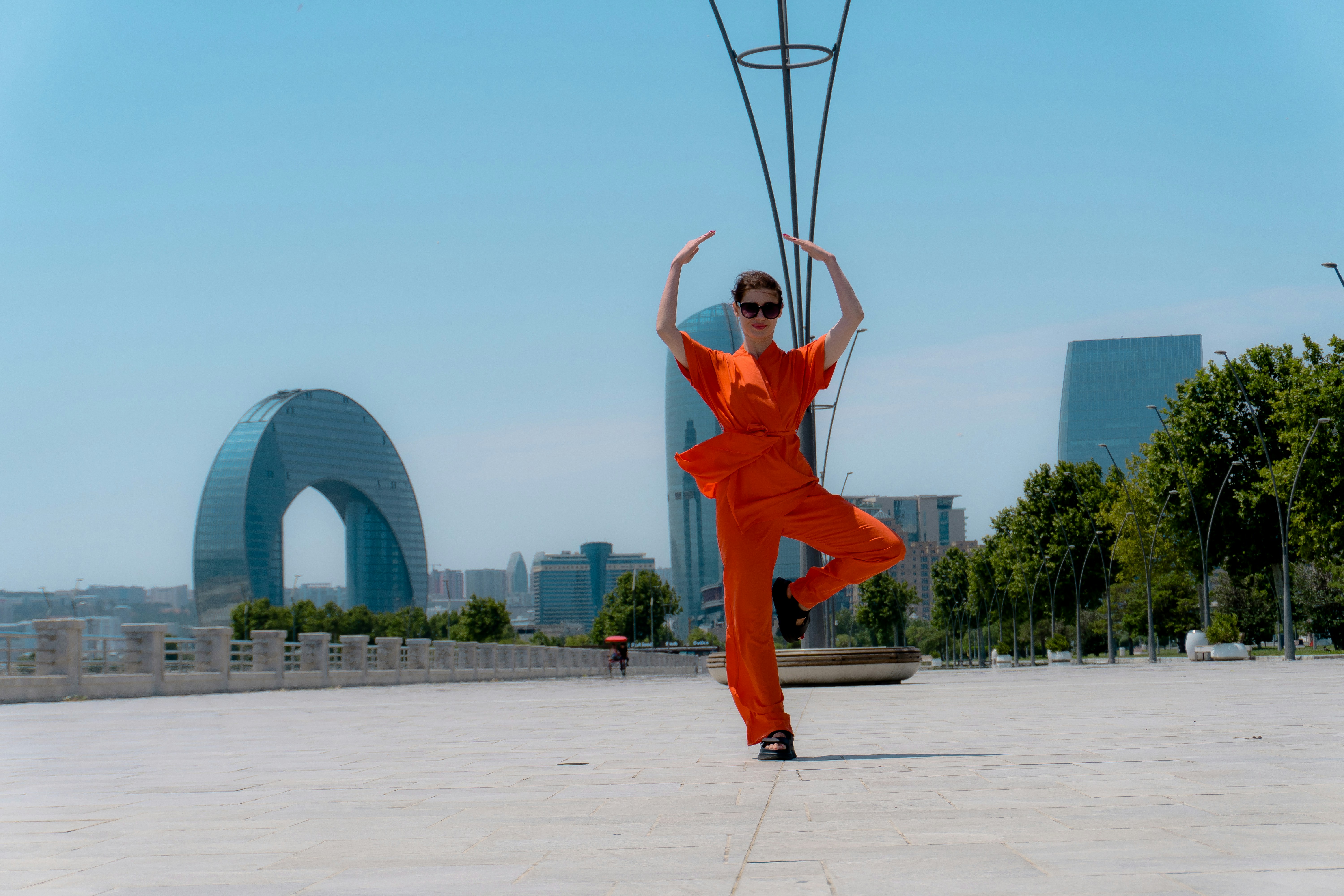 Under the Cables and Towers: An Orange-Clad Dancer Strikes a Dynamic Pose in a Sunlit City Plaza