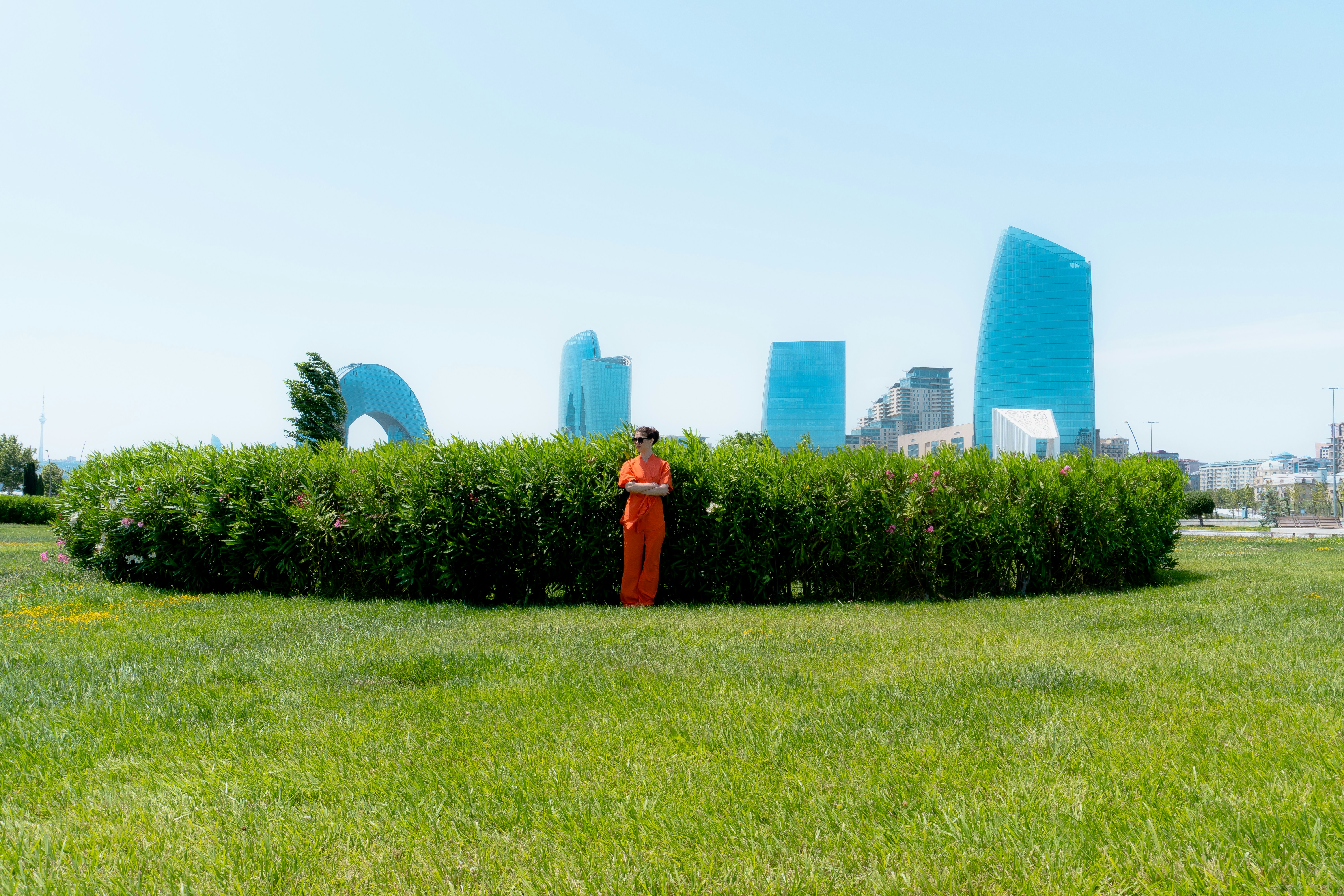 Orange-Clad Figure Framed by Hedge and Azure Skyscrapers