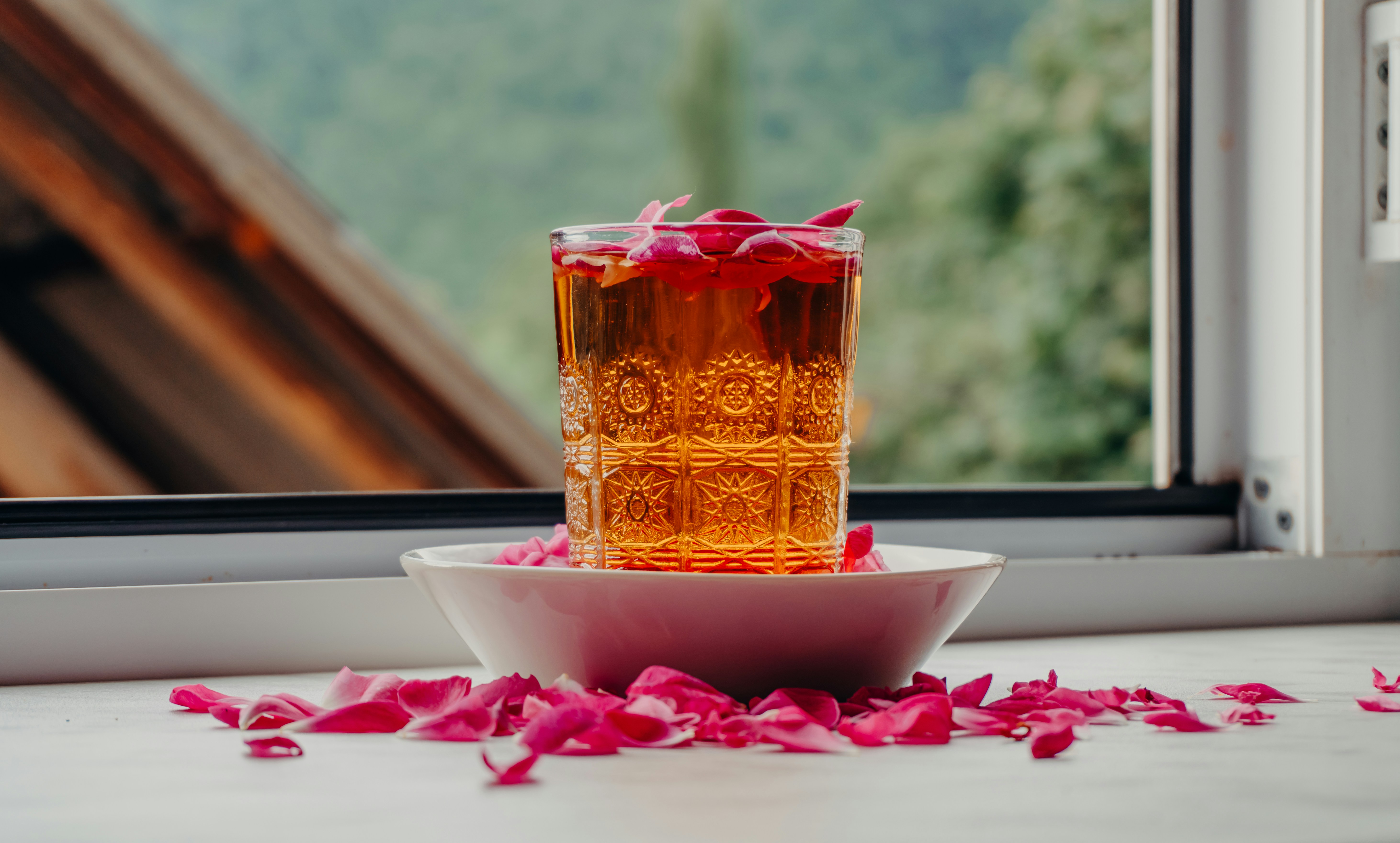 Glass of tea with rose petals on windowsill