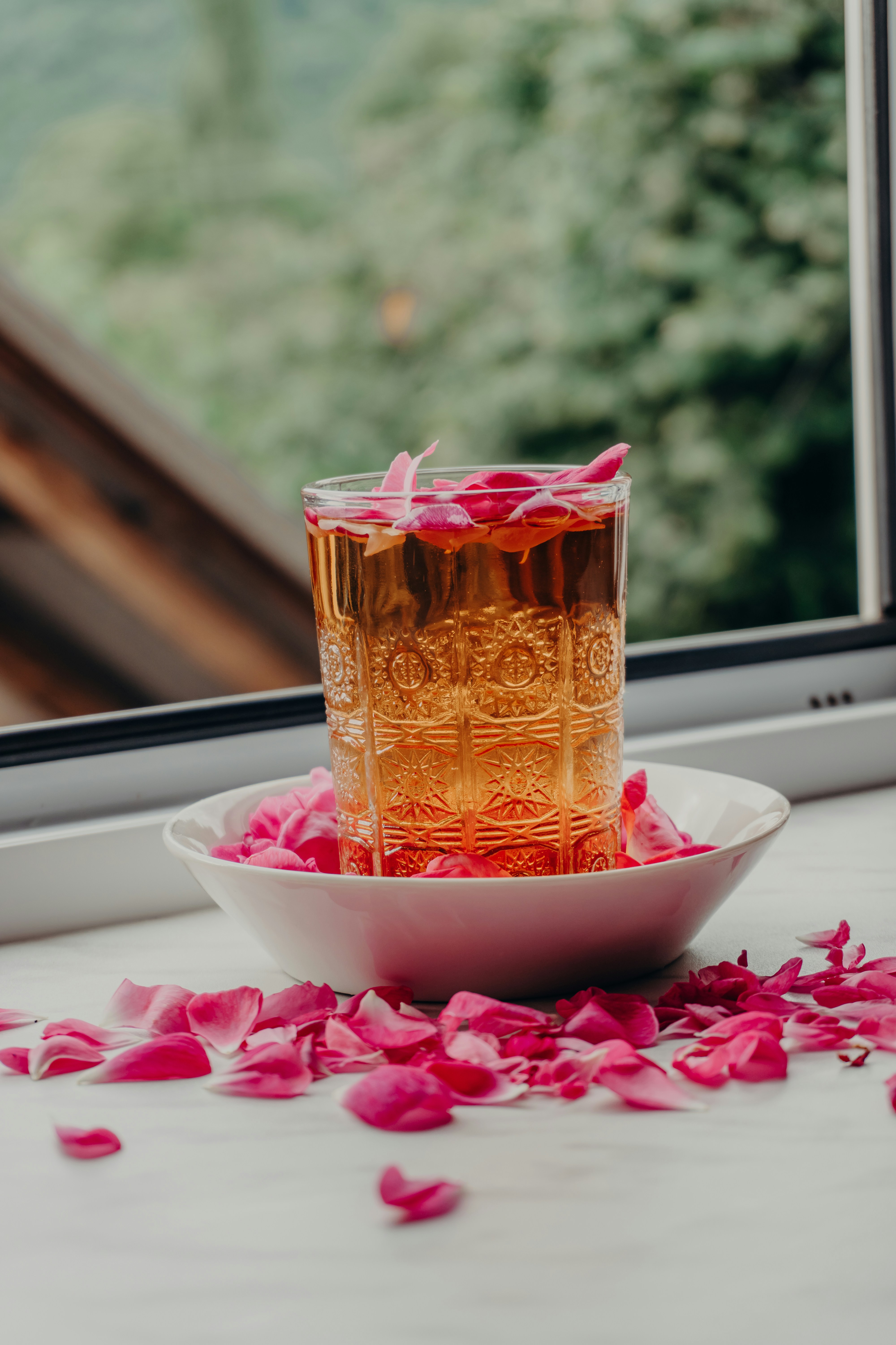 Amber Tea in a Carved Glass Framed by Rose Petals on a Windowsill