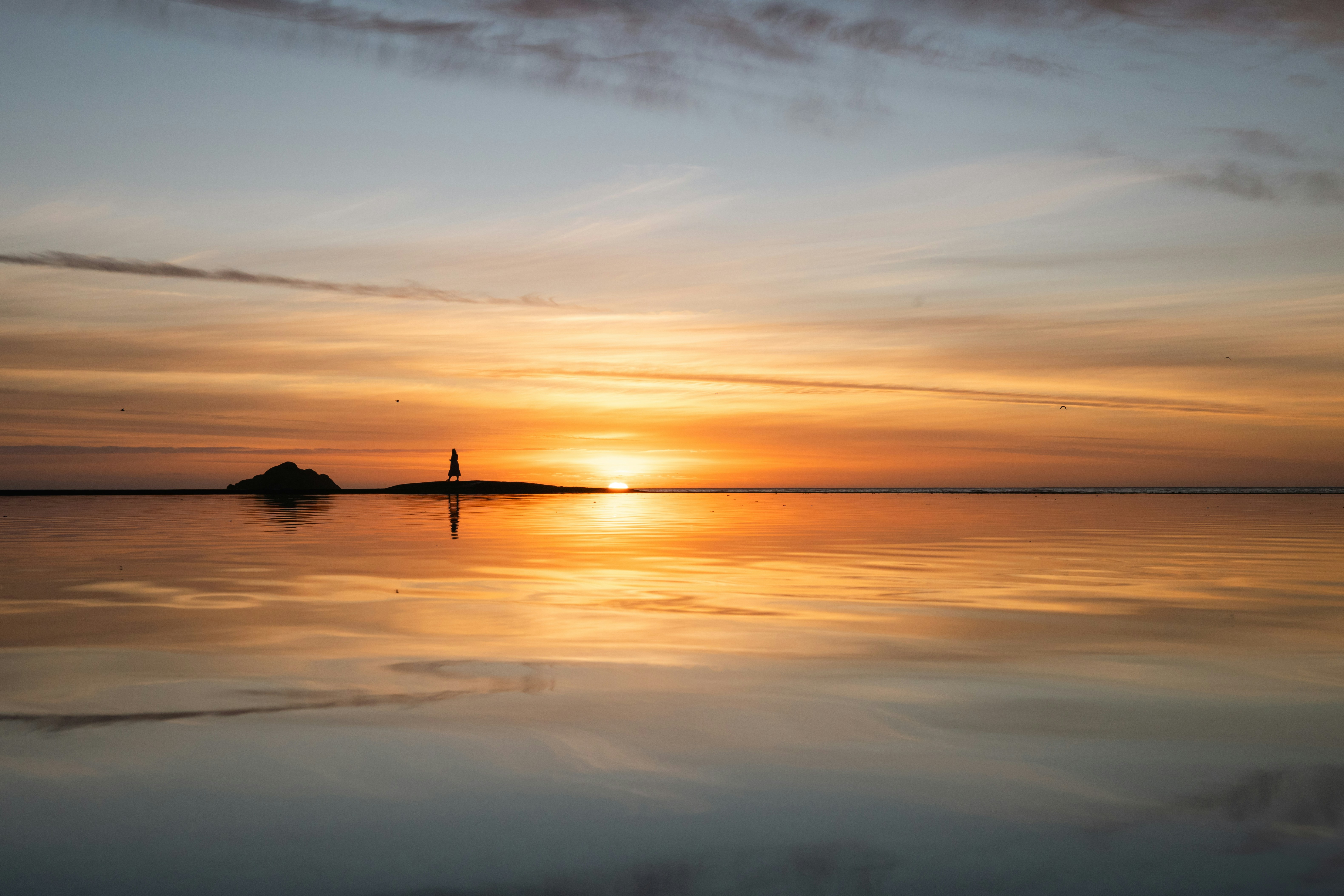 Serene sunset reflecting on calm waters with a distant silhouette of a lighthouse on a small island.
