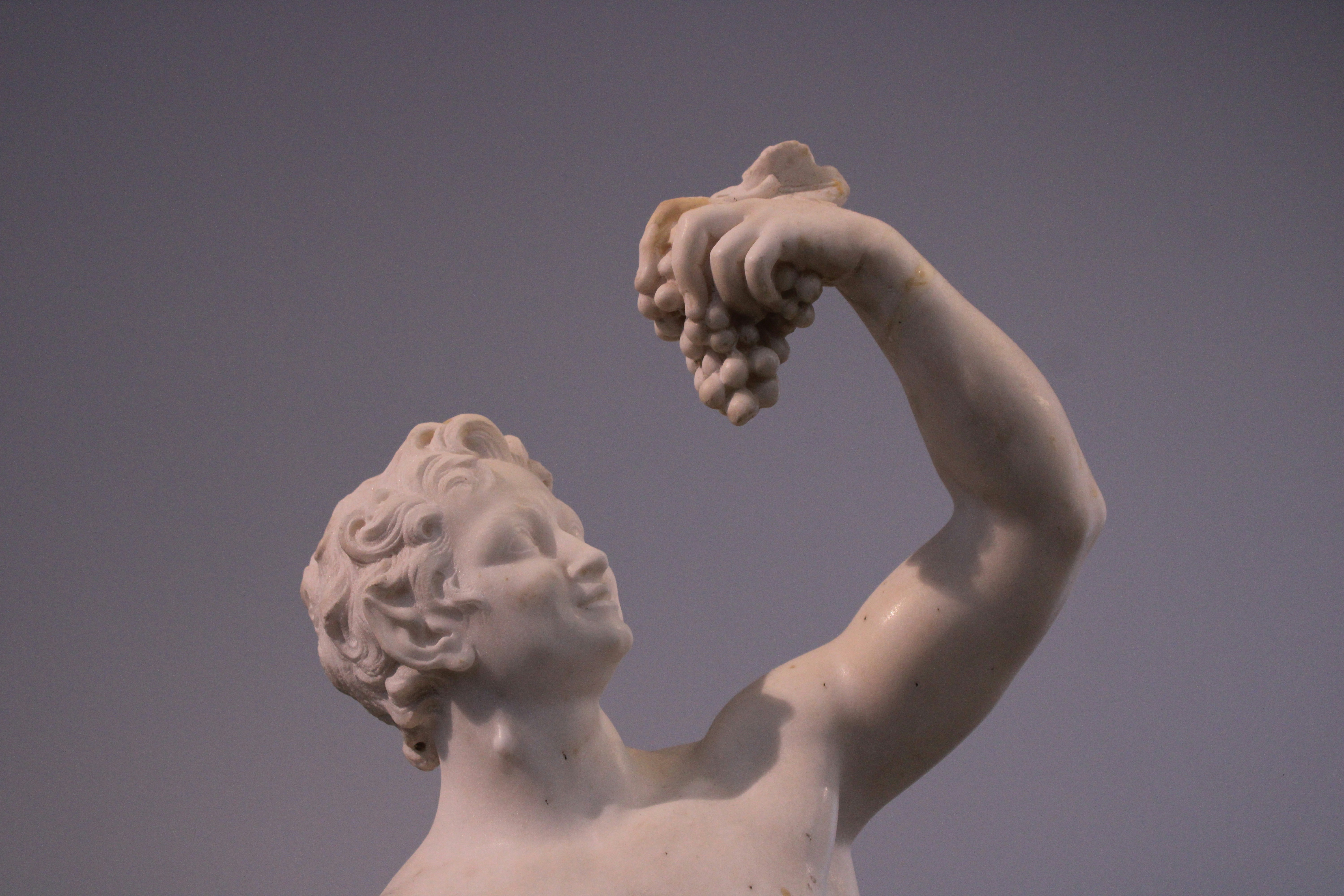 Classical marble sculpture of a youthful figure holding a bunch of grapes, symbolizing abundance and festivity.