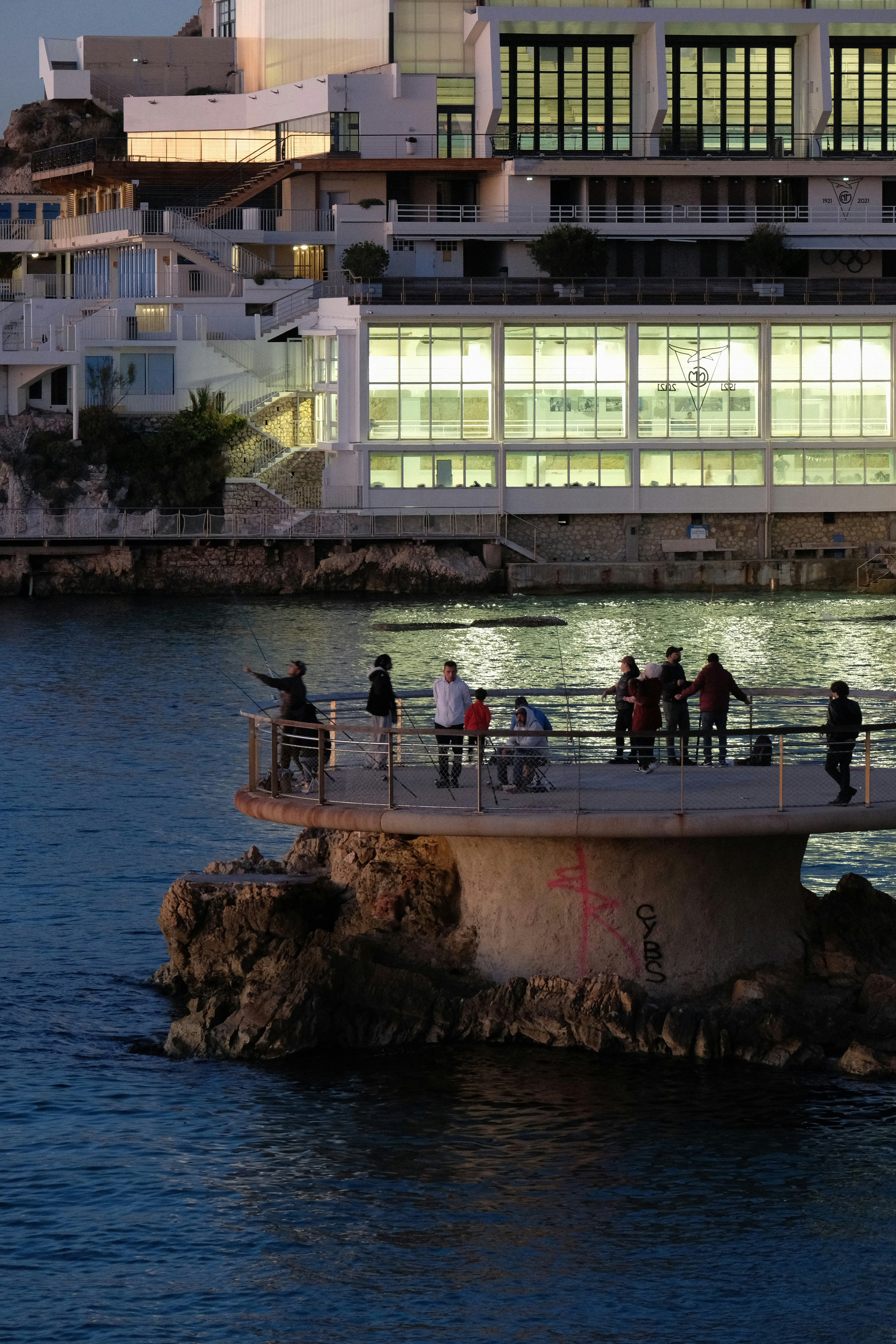 Harbor Ring: A Circular Rock Platform Crowded with Friends Near a Modern Waterfront