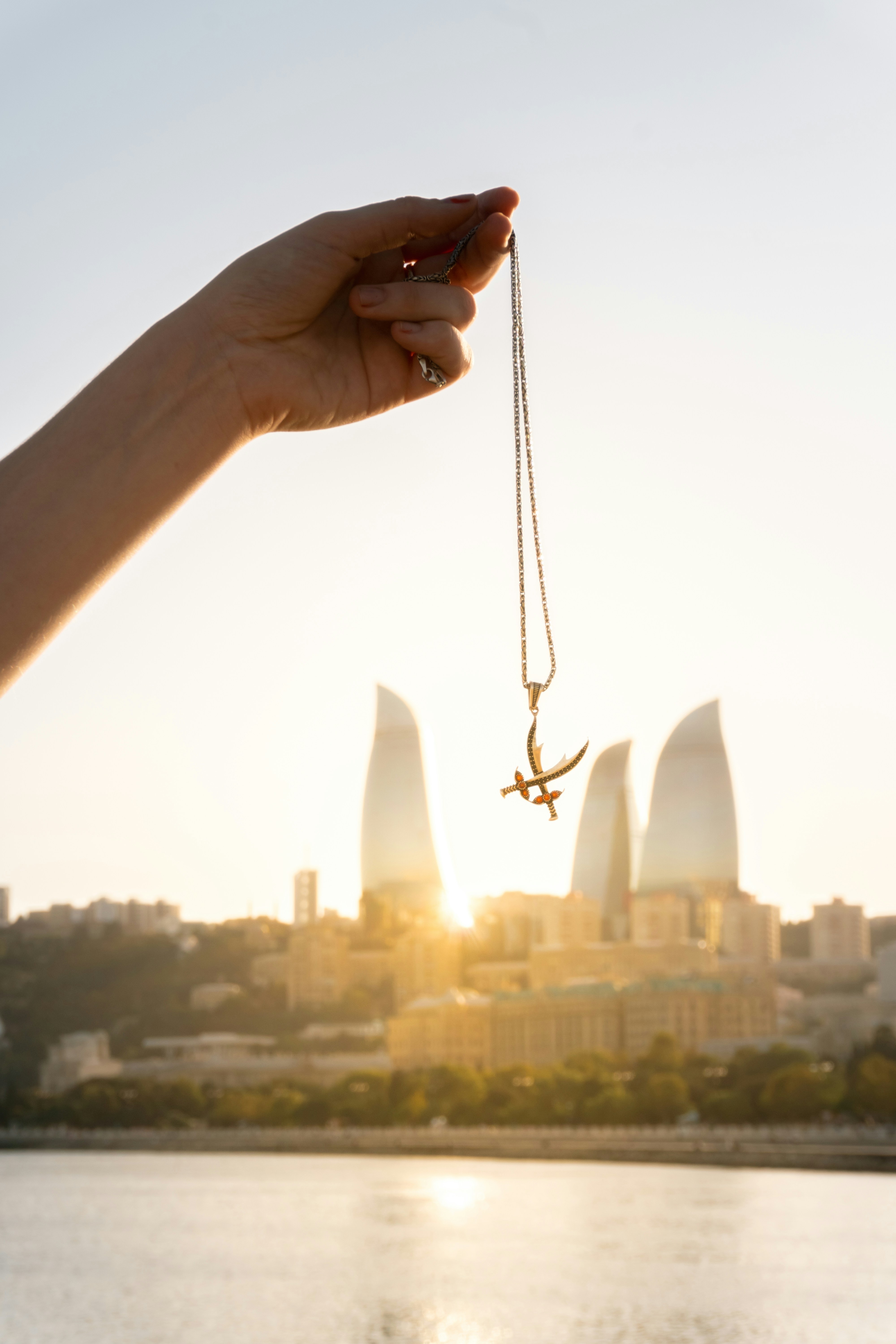 Pendant in the Sunset: Airplane Charm Raised Against a City Horizon