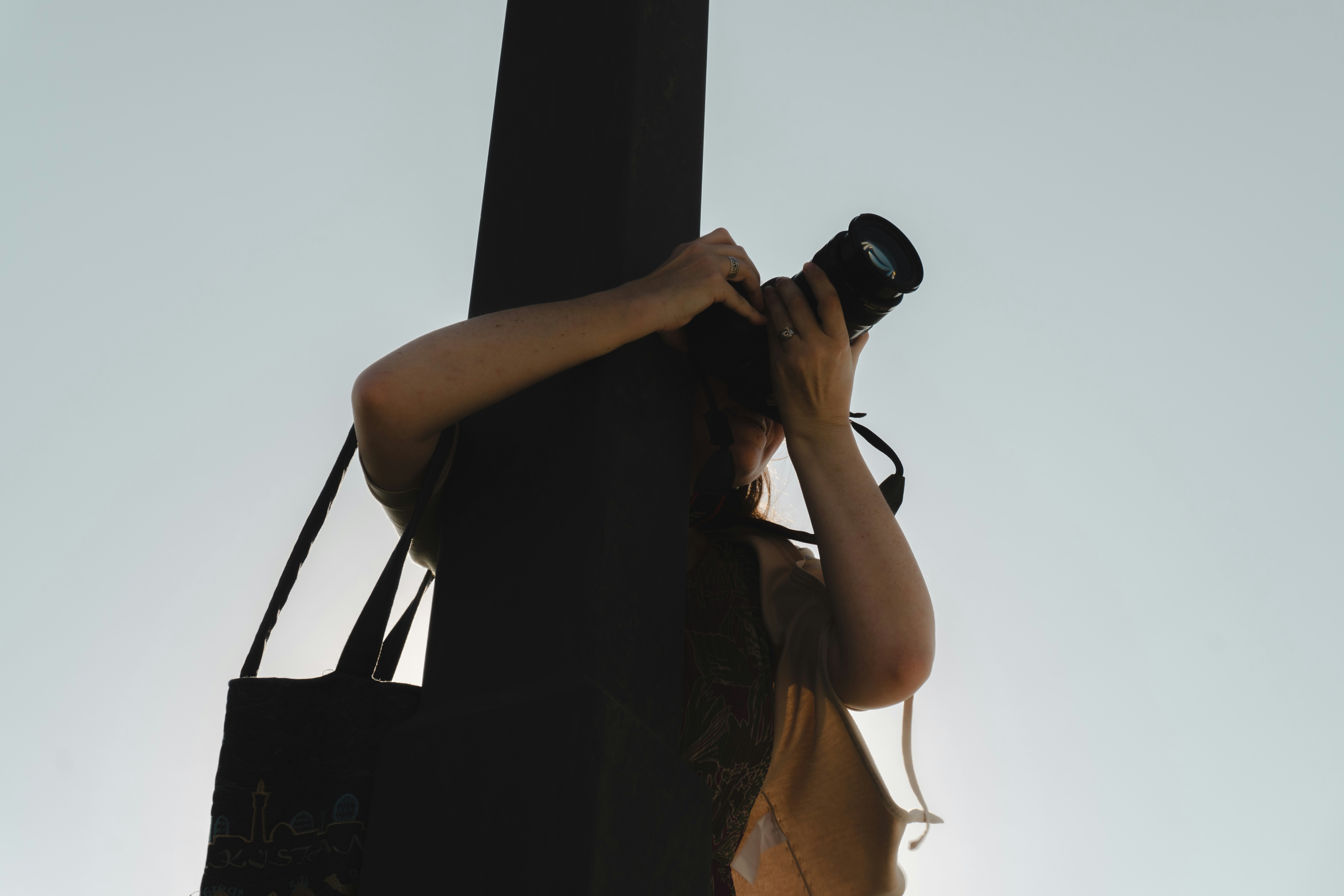 Leaning into Light: Silhouette of a Photographer Against a Pale Sky