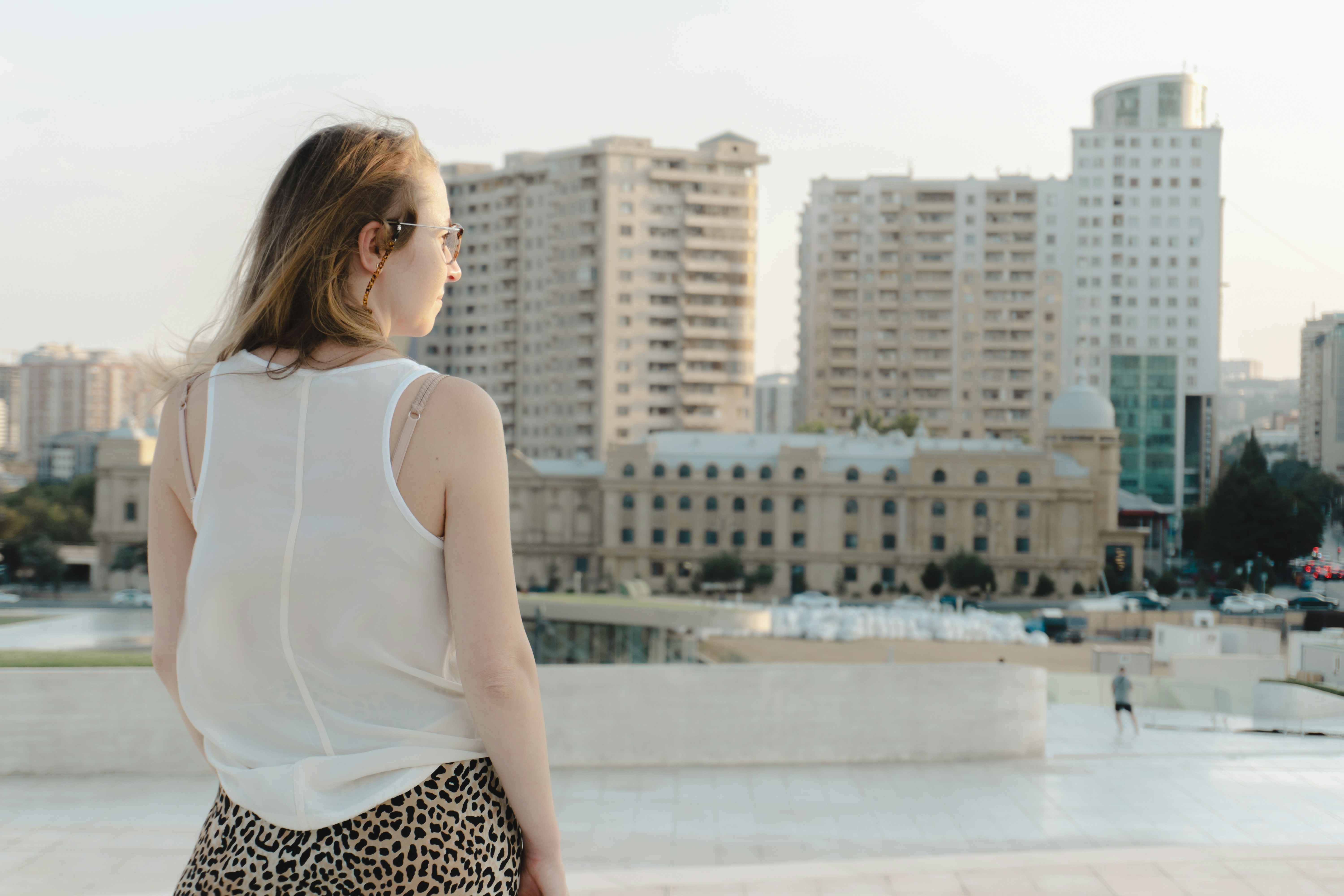 Evening Promenade: A lone observer in white gazes toward a skyline of glass and concrete.